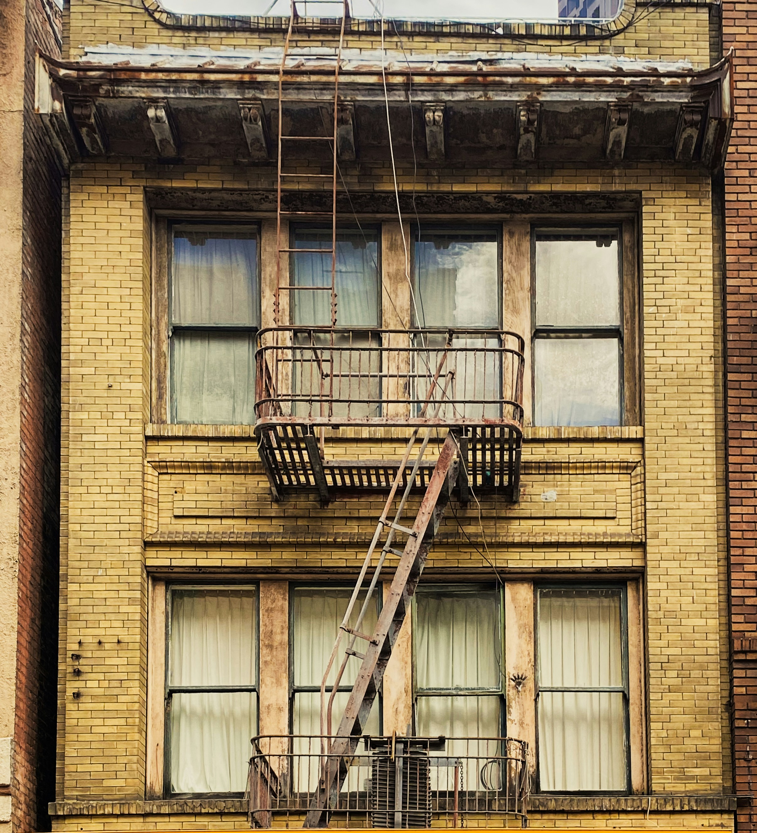 Rusted Ladder Ascends the Brick Facade, Framing a Sunlit Fire Escape