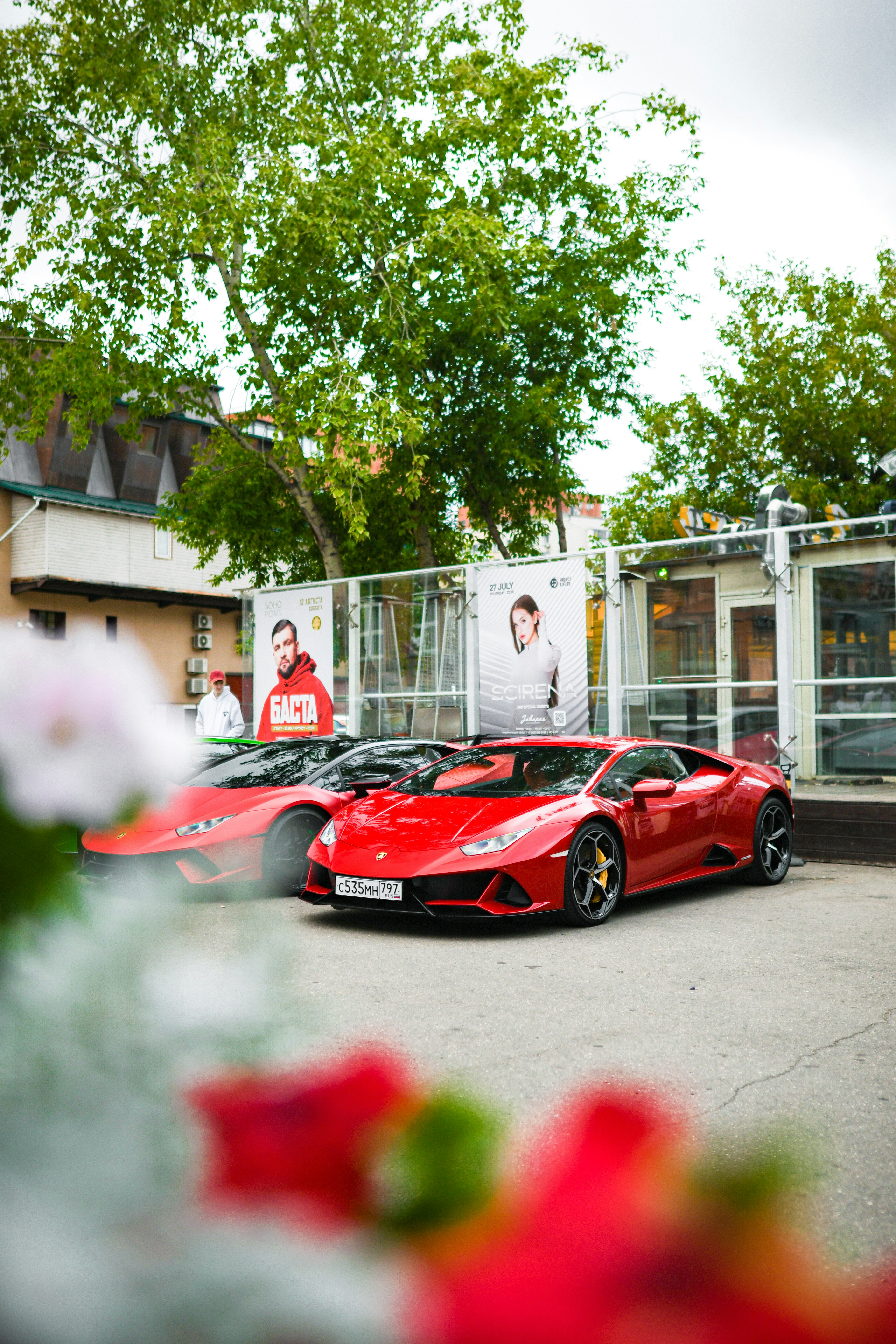 Redline in the City Square: Twin Ferraris Framed by Posters and Trees