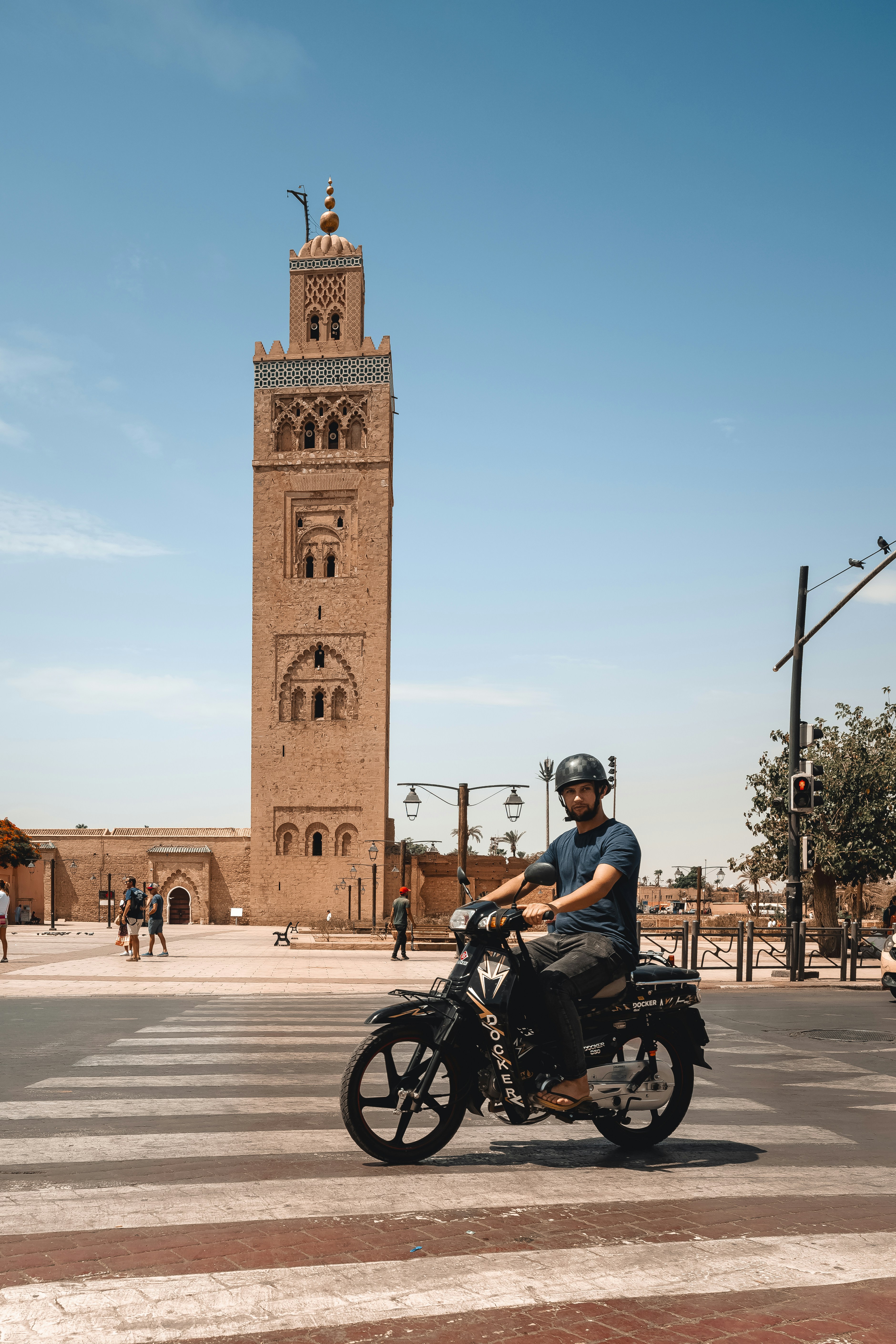 a man riding a motorcycle down a street next to a tall tower
