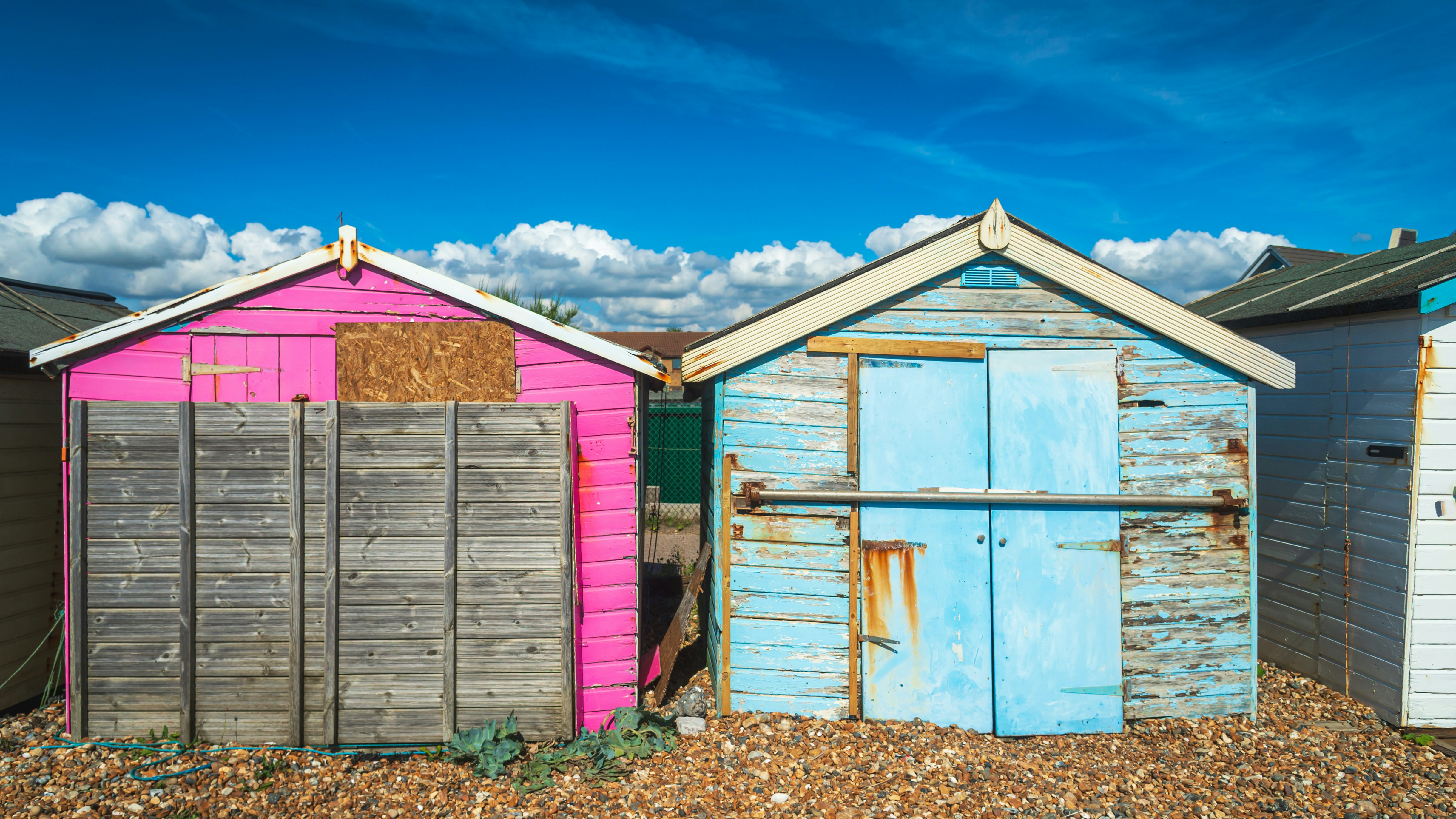 Brightly colored beach huts with peeling paint under a vivid blue sky.