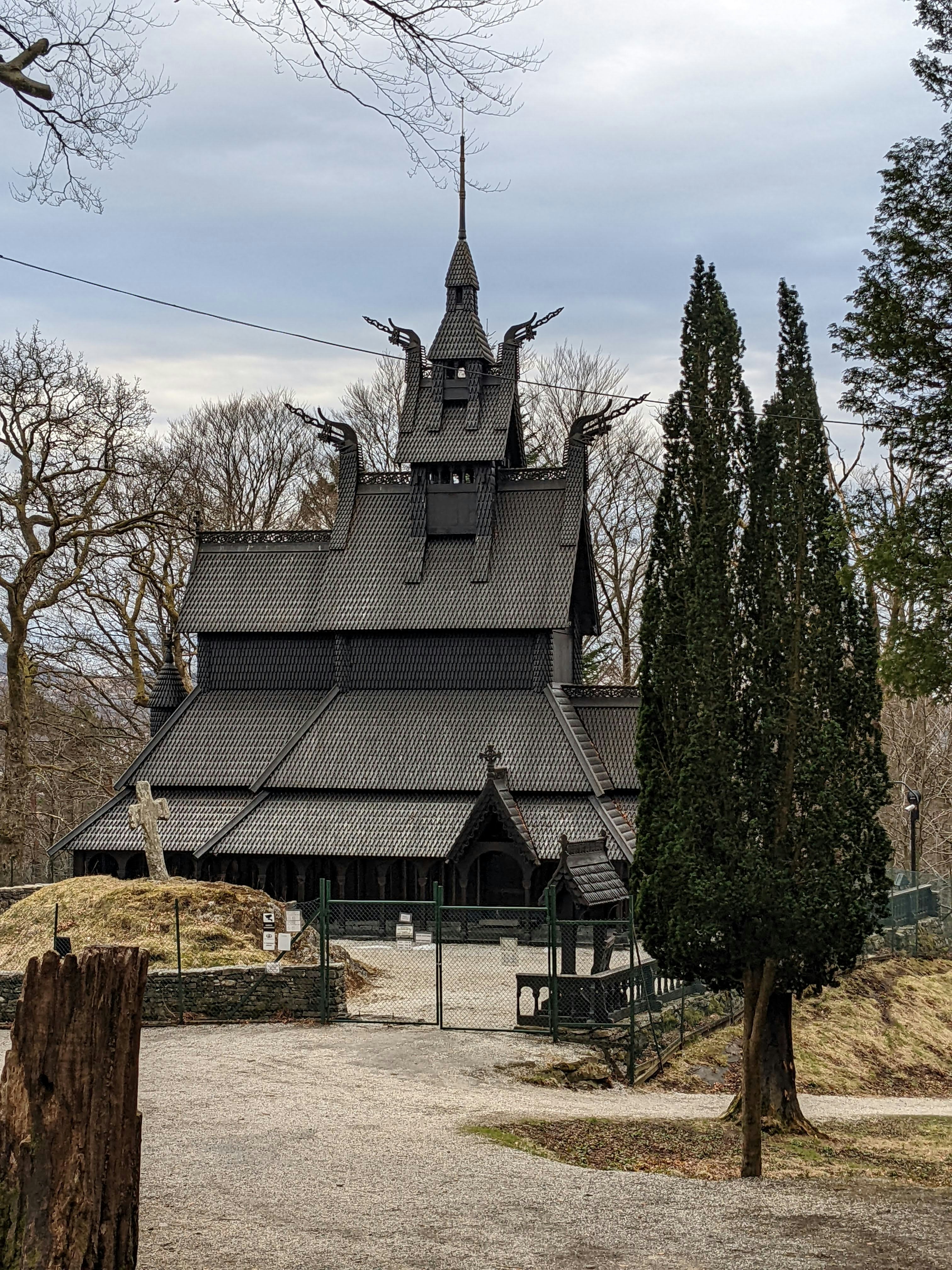 Intricately designed stave church with dark wooden architecture surrounded by trees and a gravel path.