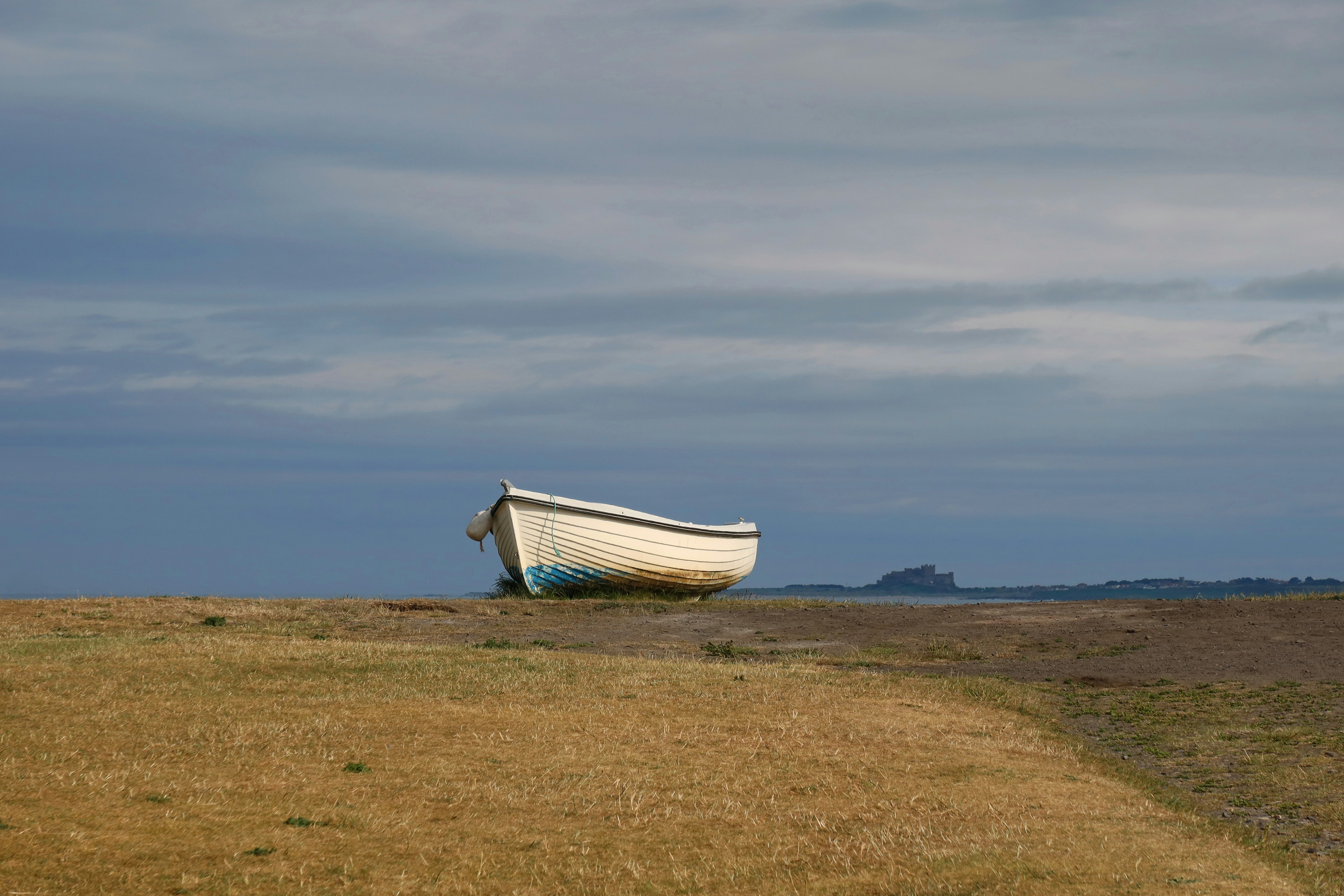 A weathered boat rests on a grassy expanse under a moody sky, hinting at stories of past journeys. The distant silhouette of a castle adds a sense of history.