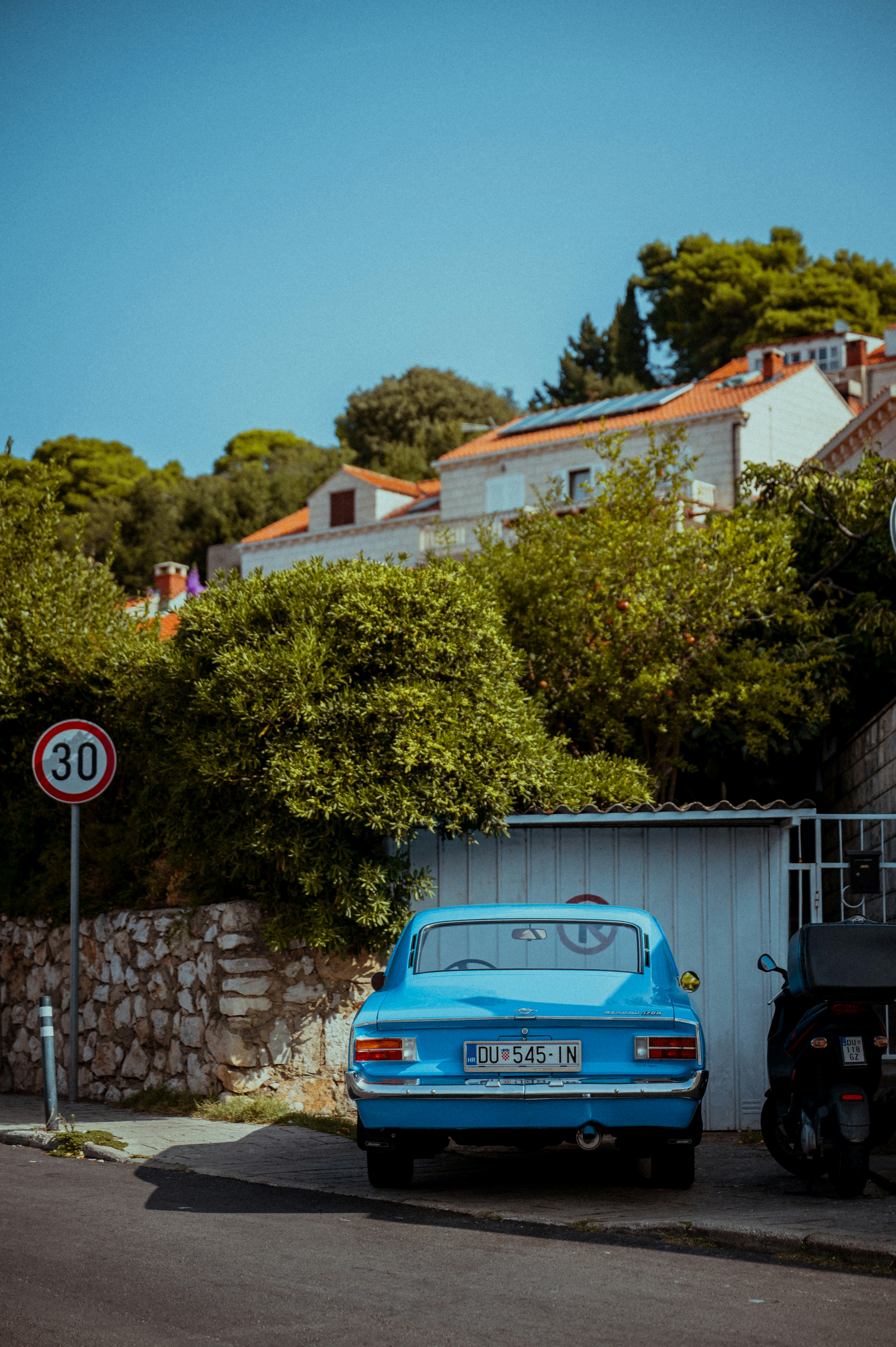 Pastel-blue sedan tucked beneath a sunlit hillside, framed by lush greenery