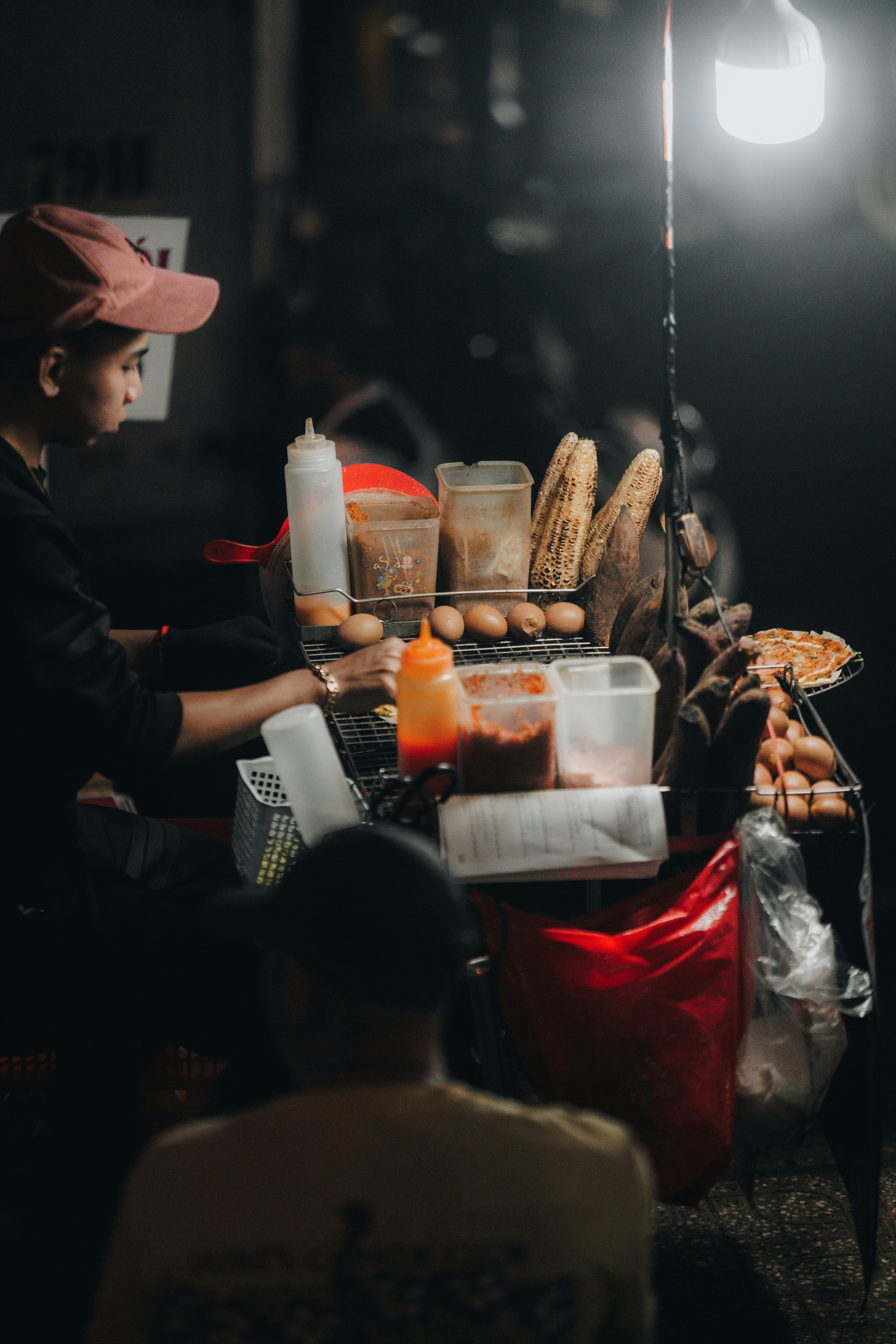 Haloed Night Market Stall: Eggs, Corn, and Condiments Under a Lone Glow