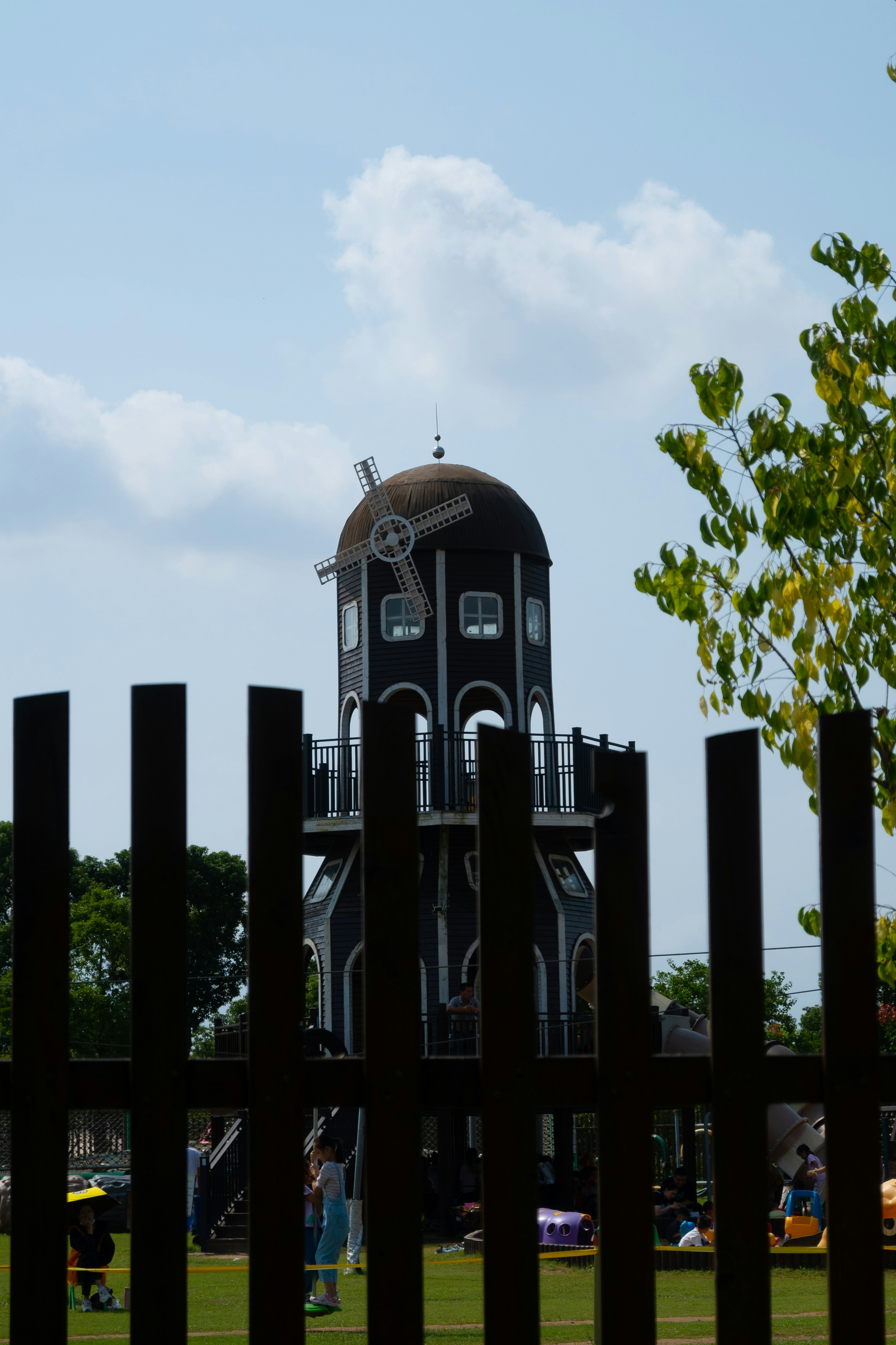 Windmill Play Structure Rising Above a Wooden Fence in a Sunlit Park