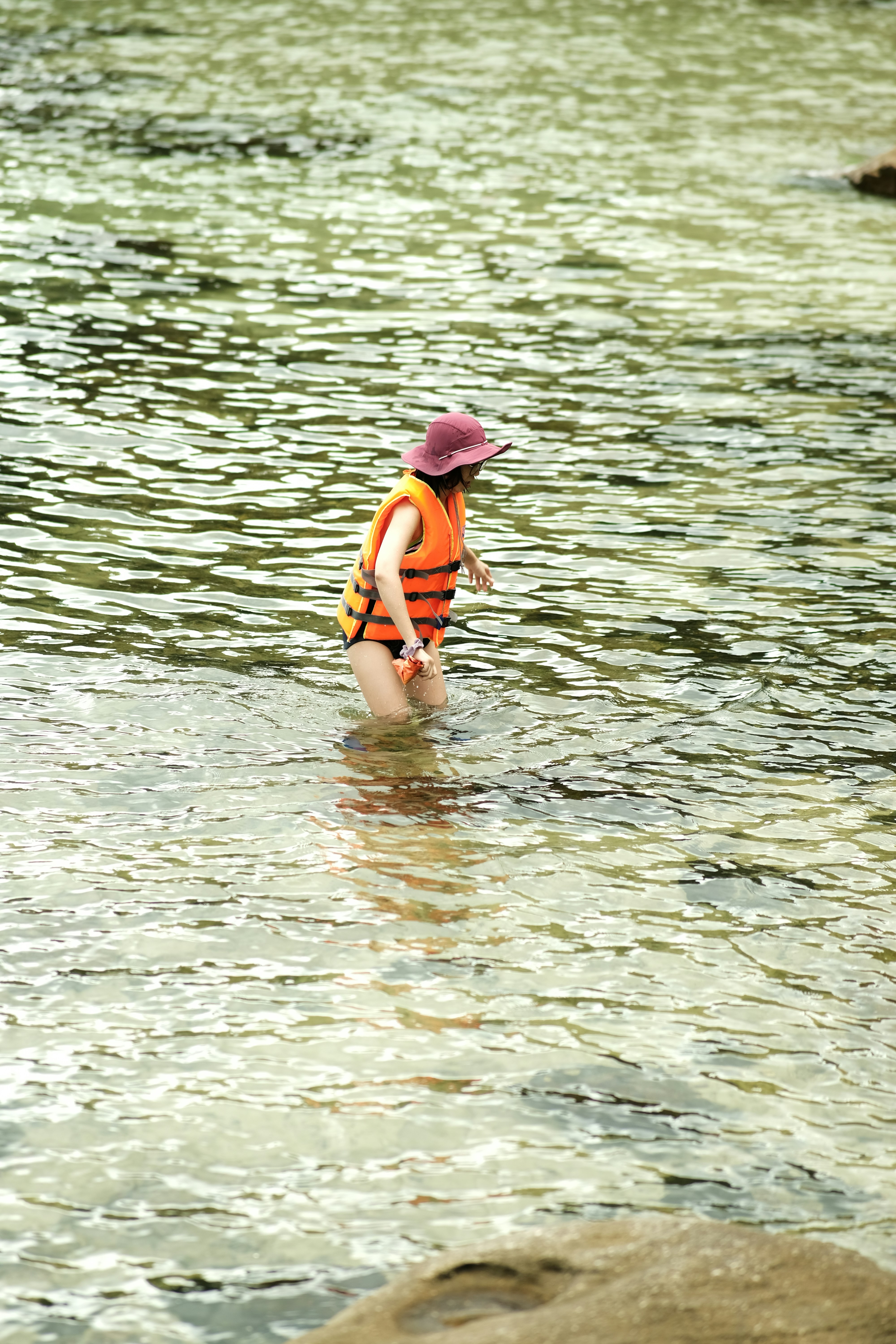 Sunlit Shallows: A Small Figure in an Orange Life Jacket Wading a Quiet River