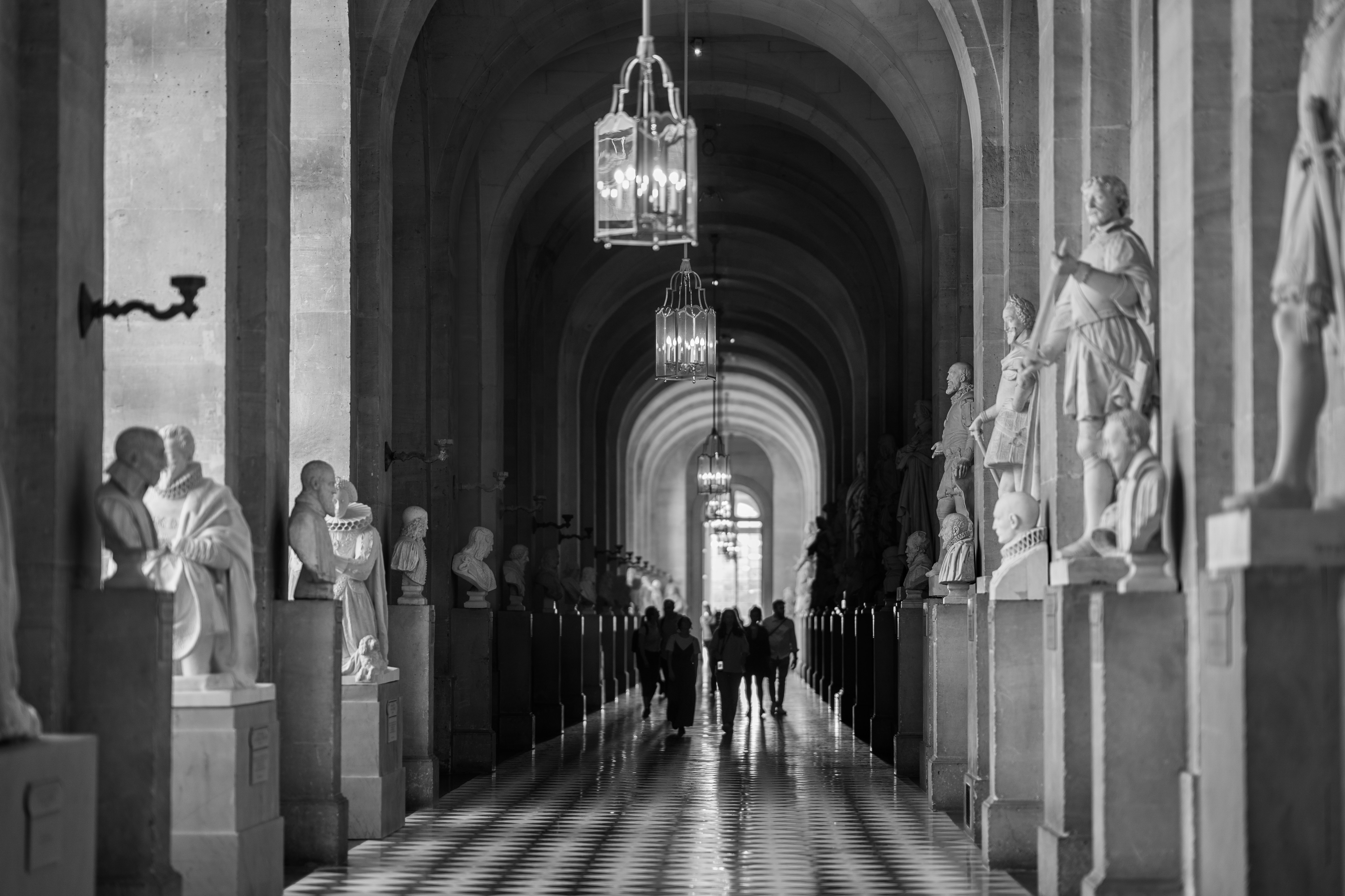 Black and white hallway with statues lining the walls under arched ceilings.
