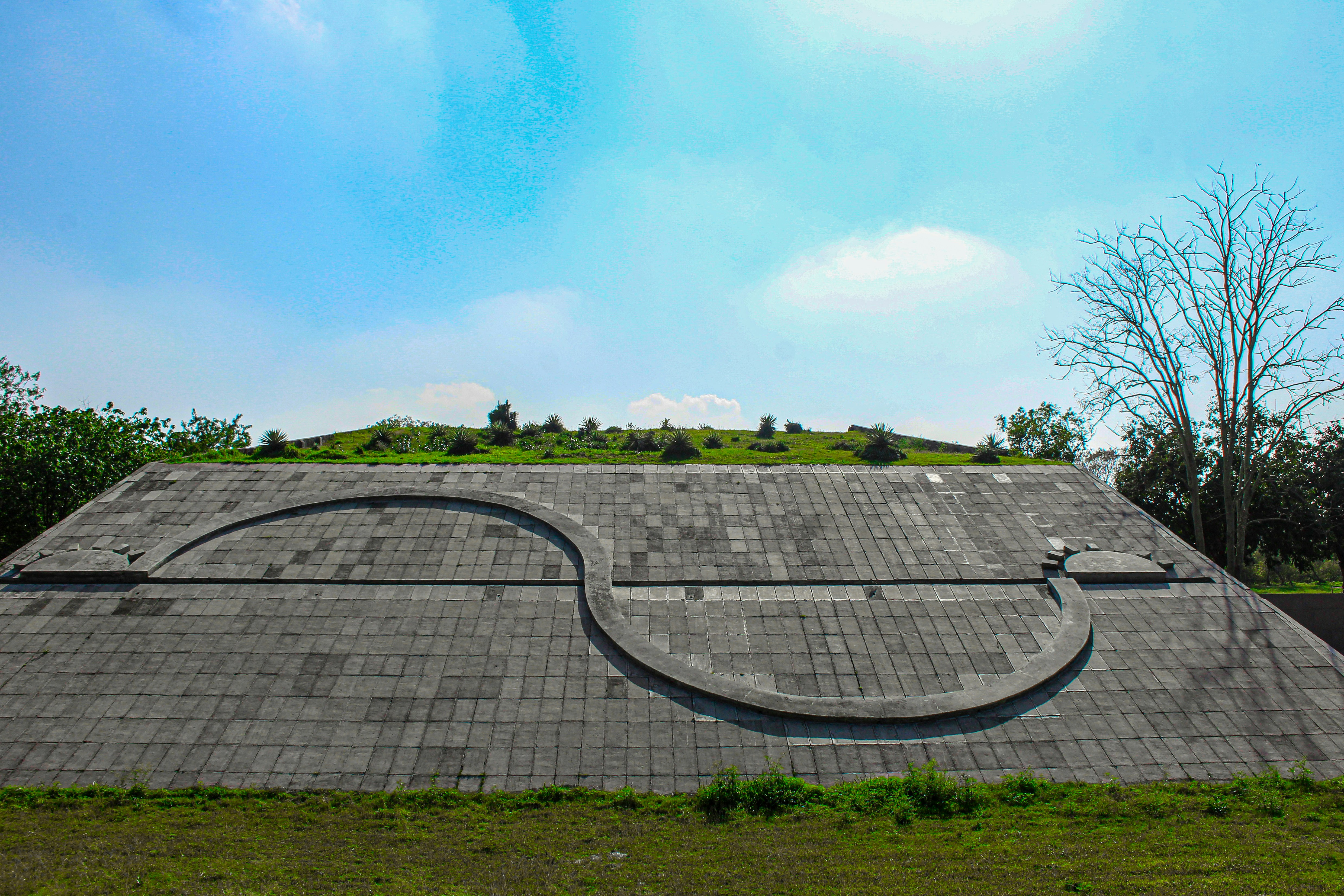 Curving black pipe on a large gray concrete slope under a bright blue sky.