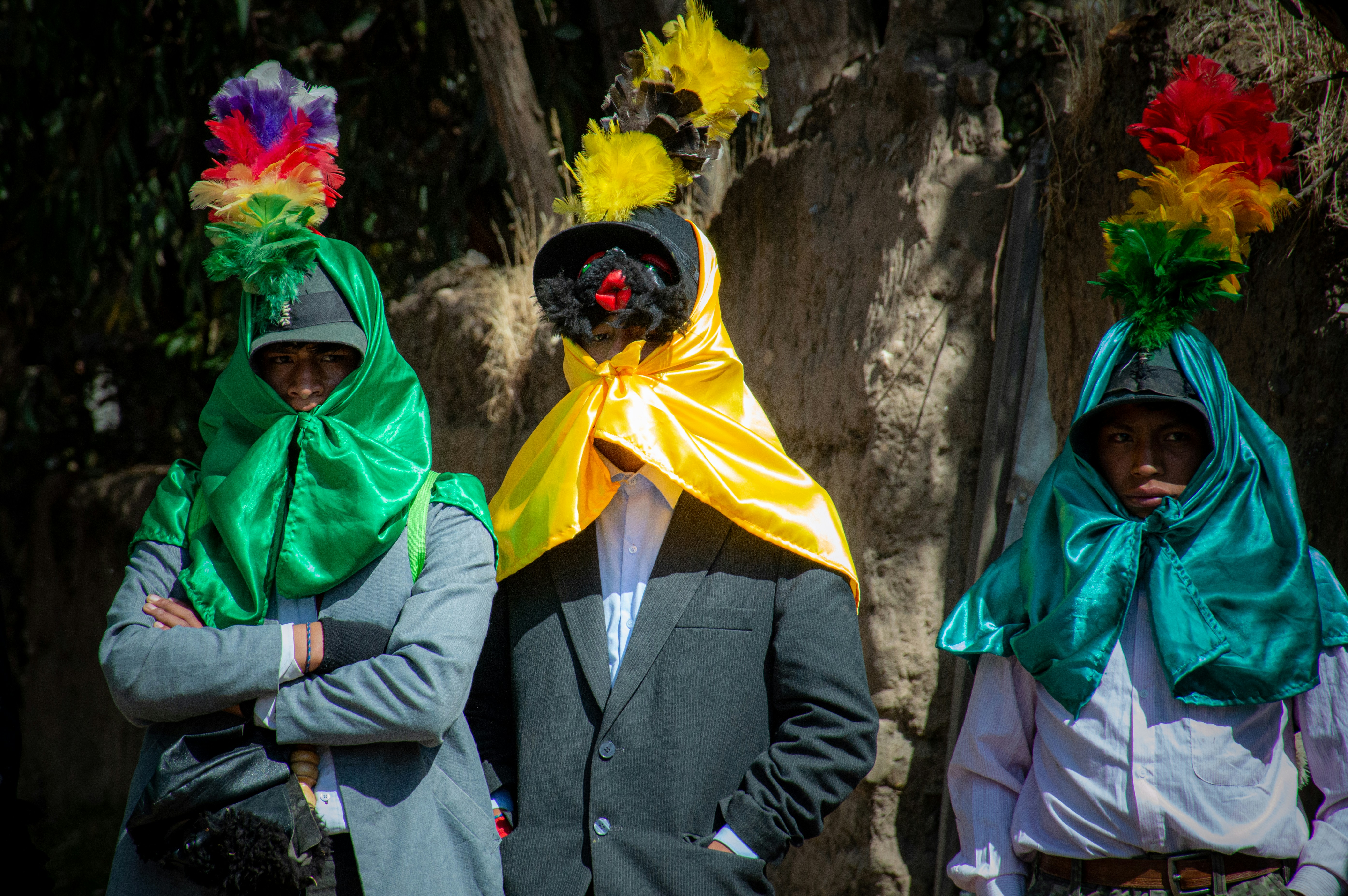 Colorful Cloak Parade: Three Costumed Figures Stand Under a Sunlit Wall