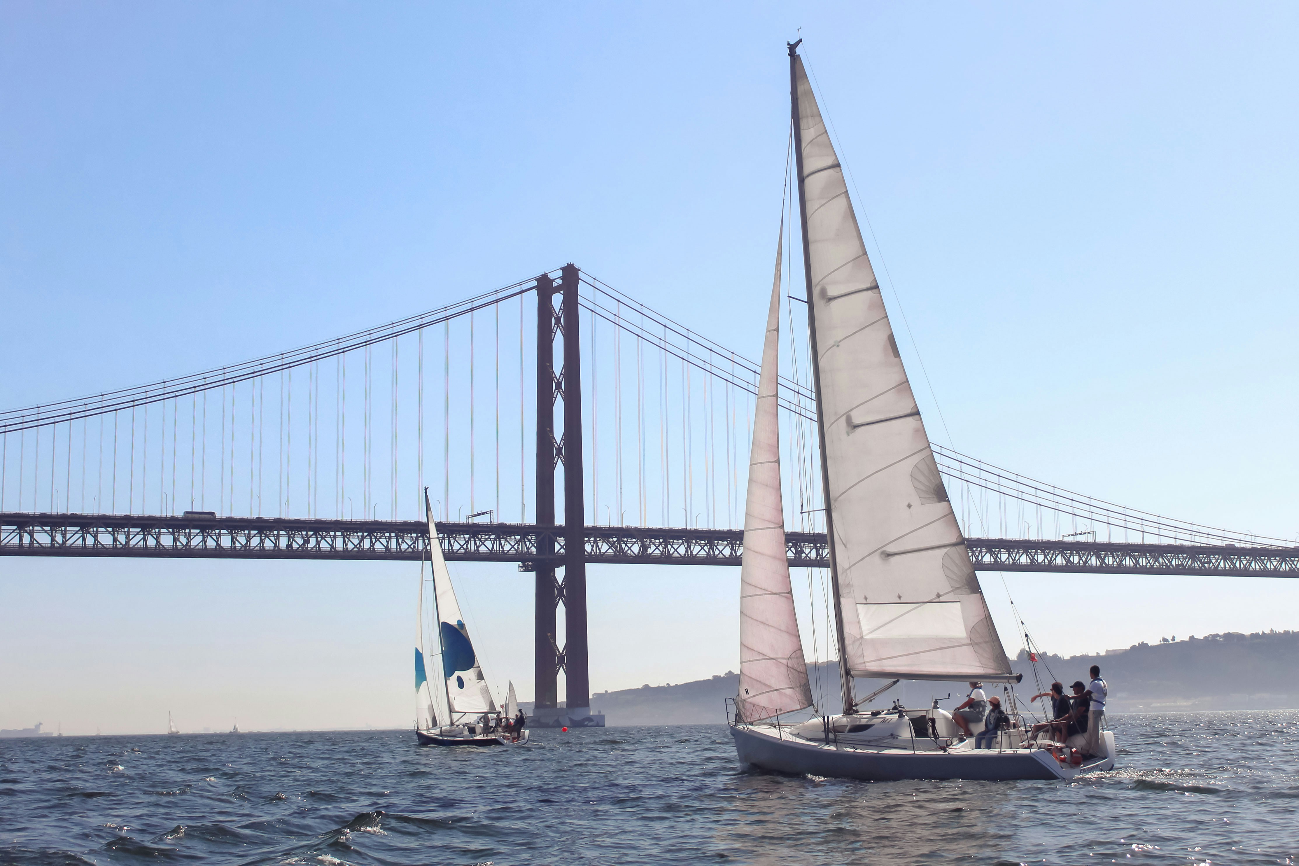 A sailboat sailing under a bridge on the water photo – Free Boat Image ...