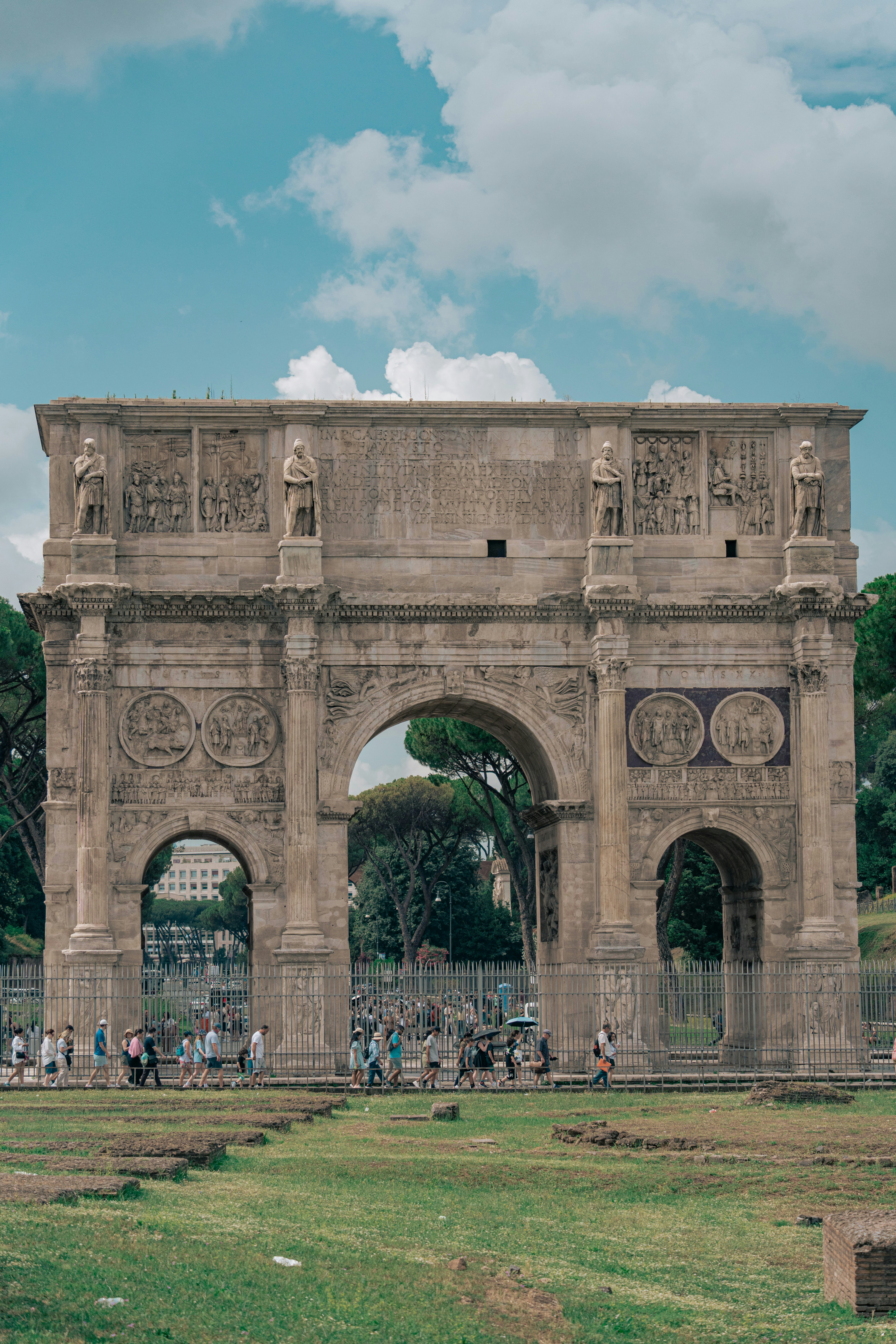 A Monumental Arch in the Park: Carved Stone and Strolling Visitors Under a Clear Sky