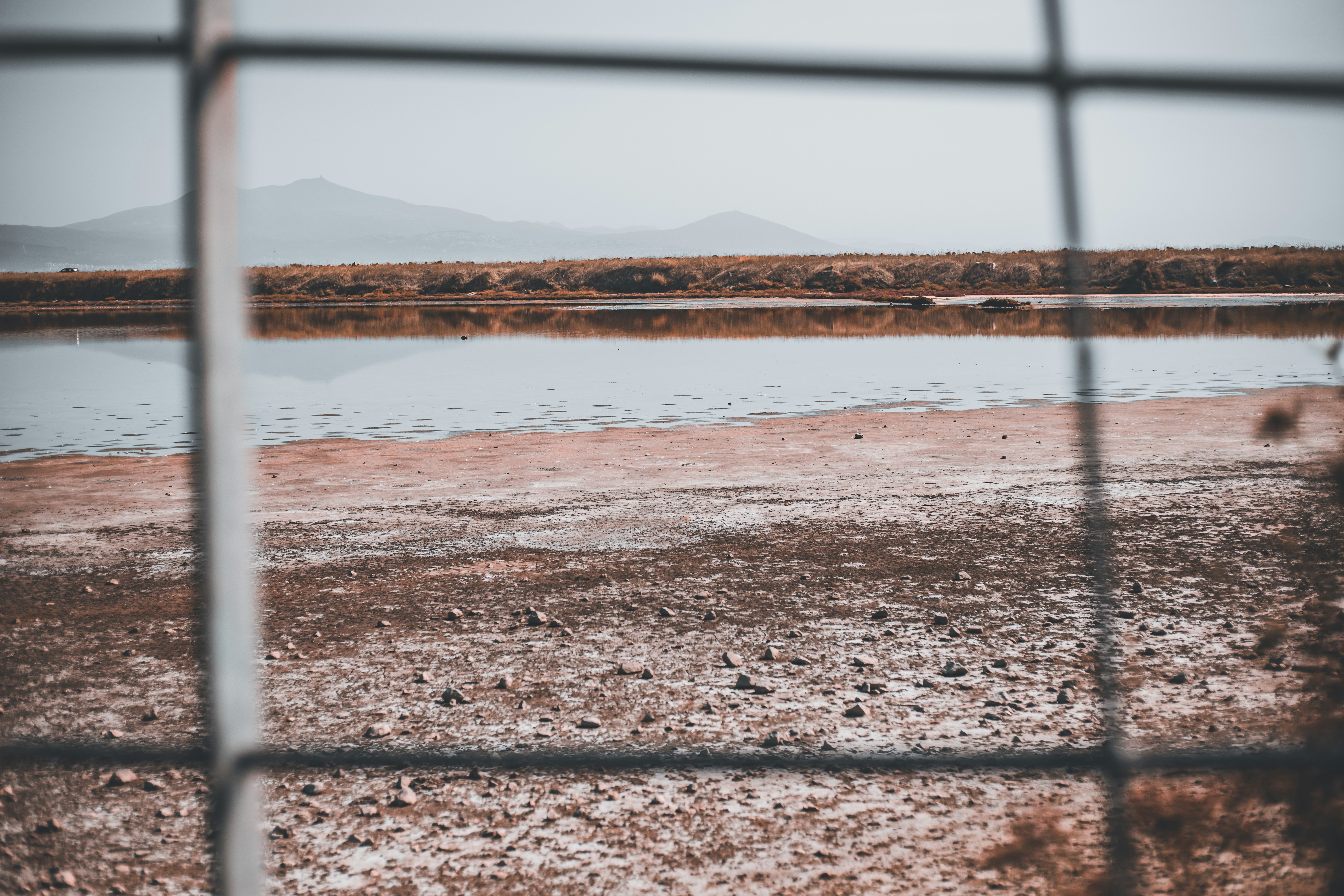 Horizon Behind the Wire: Distant Peaks Across a Salt-Flat Shore