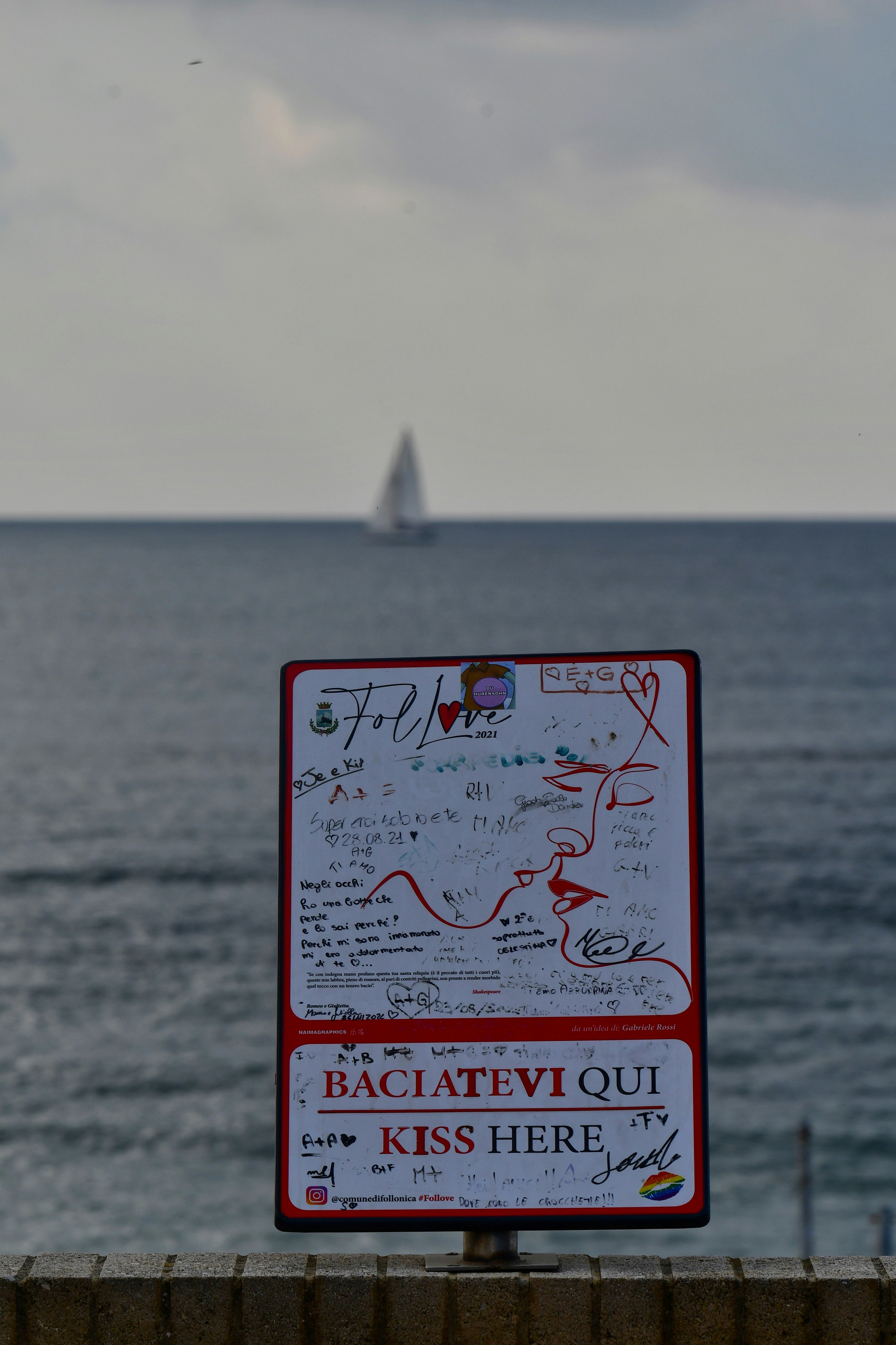 Kiss Here on the Pier: Graffiti Sign Framing a Distant Sailboat