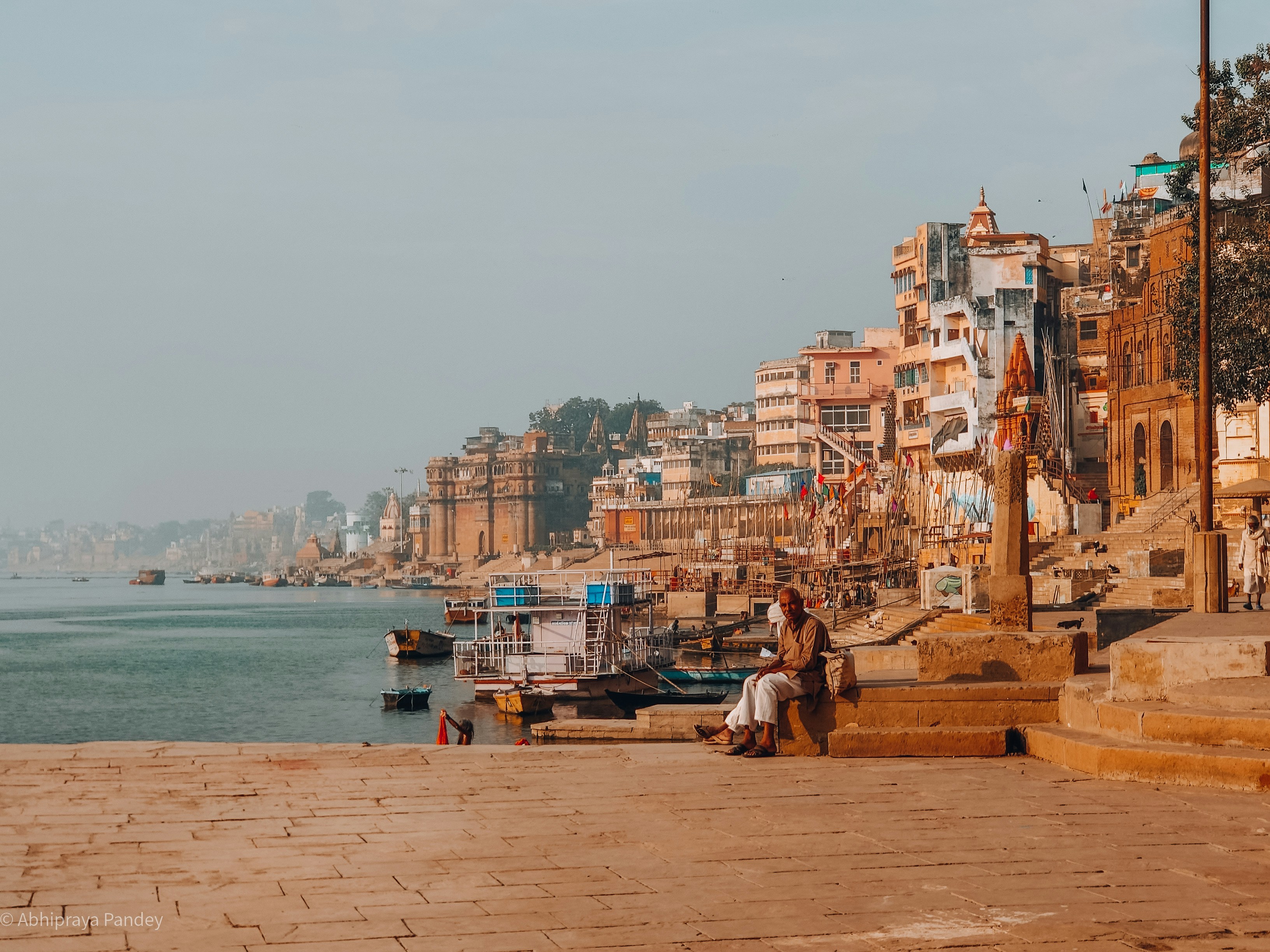 Colorful riverside buildings and boats on the Ganges under a clear sky.