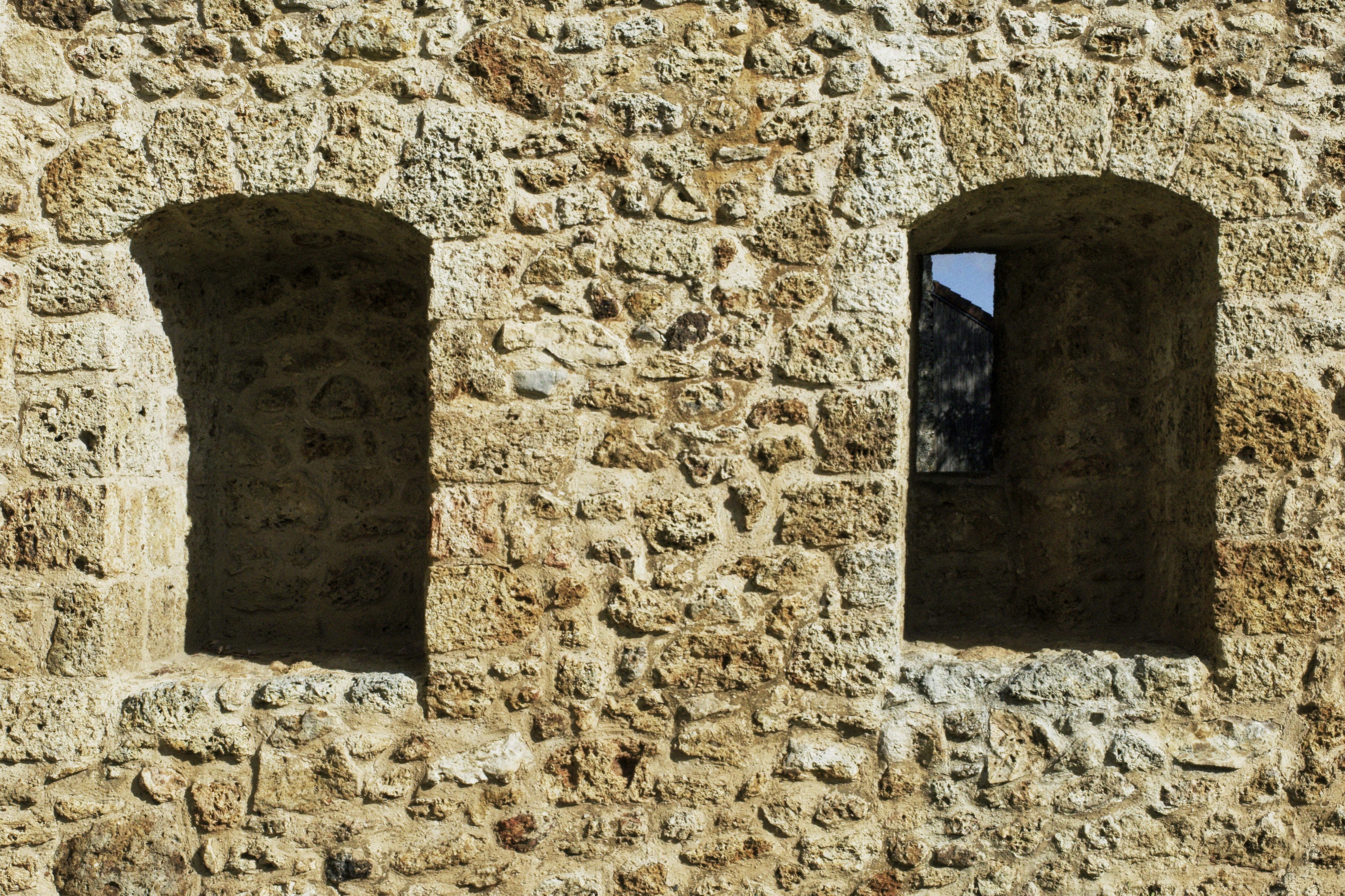 Weathered stone wall featuring two arched windows, showcasing the texture and age of the structure.