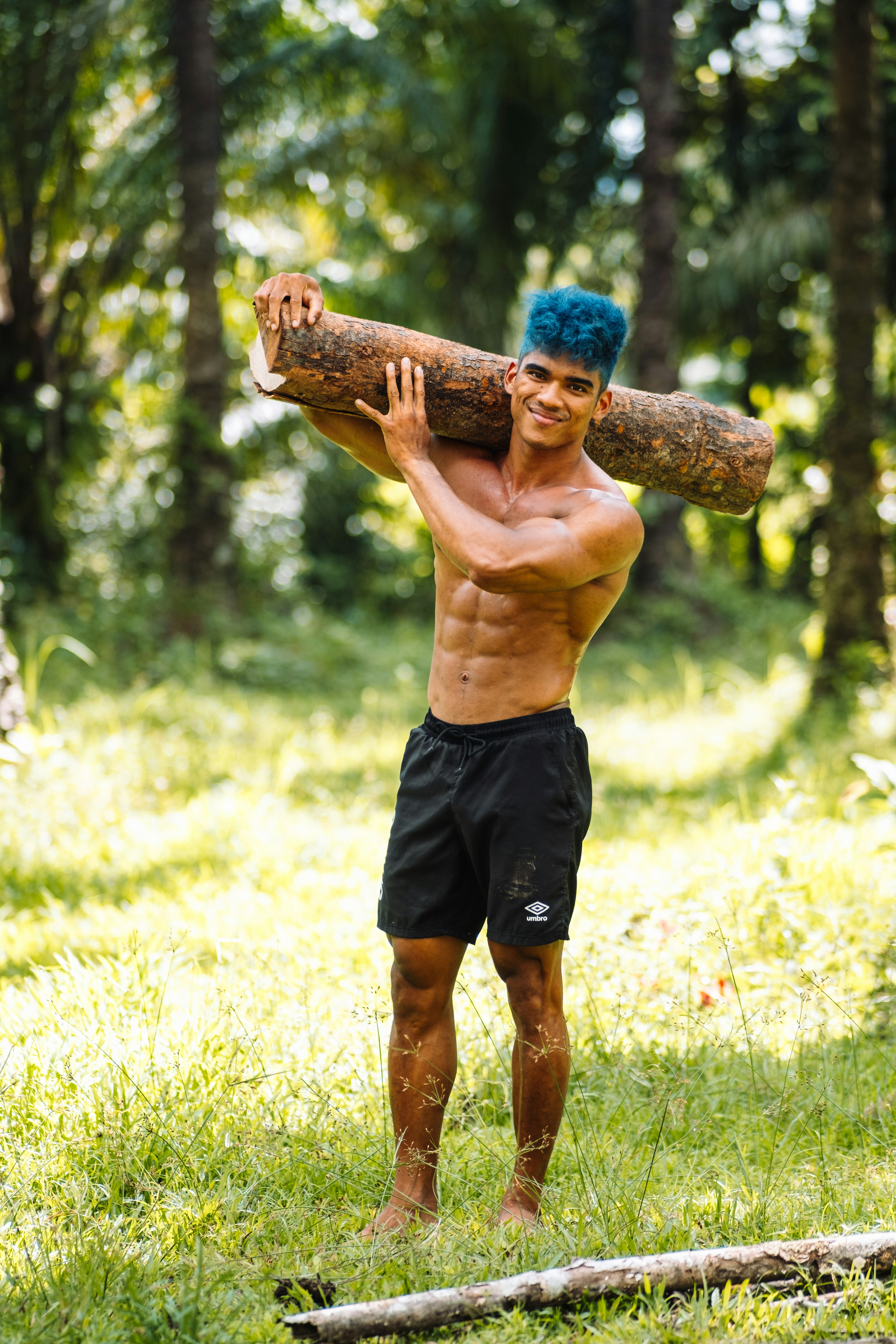 Stronglift in the Clearing: Man Lifts a Log Amid Sunlit Pines