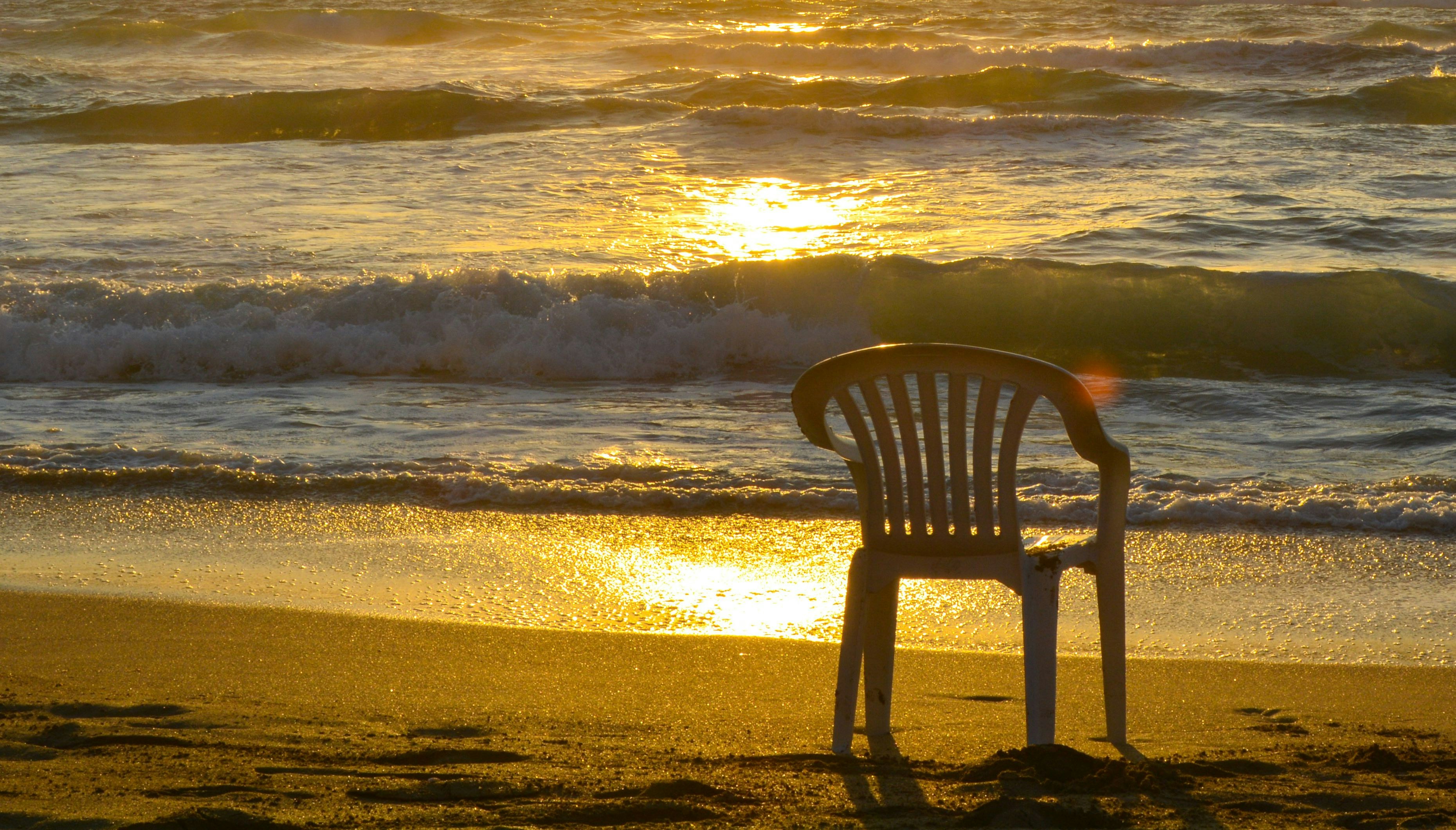 Plastic chair facing the ocean at sunset with golden light reflecting on the waves.