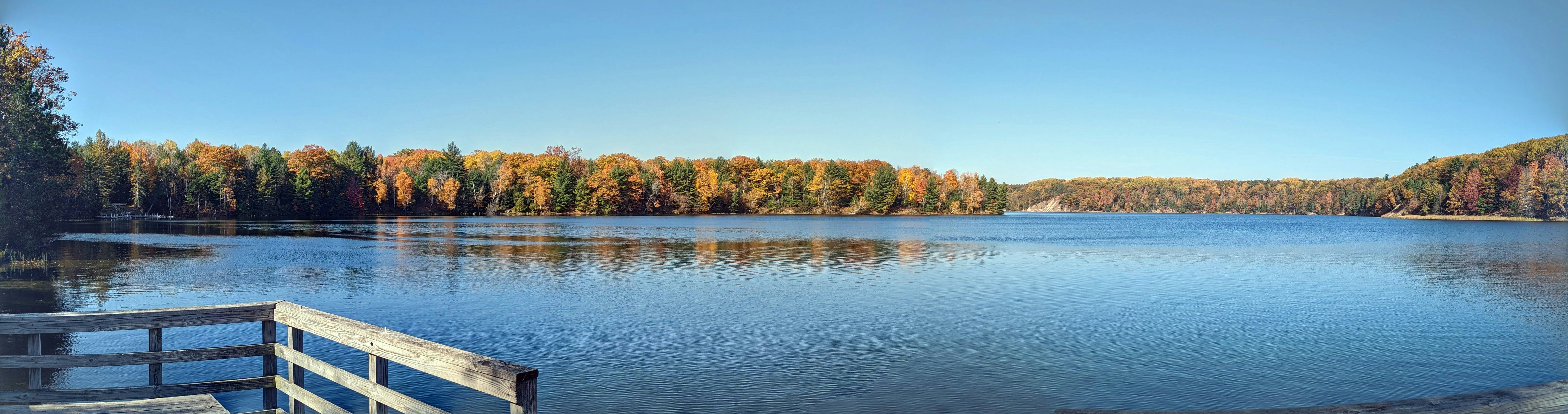 Tranquil lake reflecting vibrant autumn foliage under a clear blue sky.