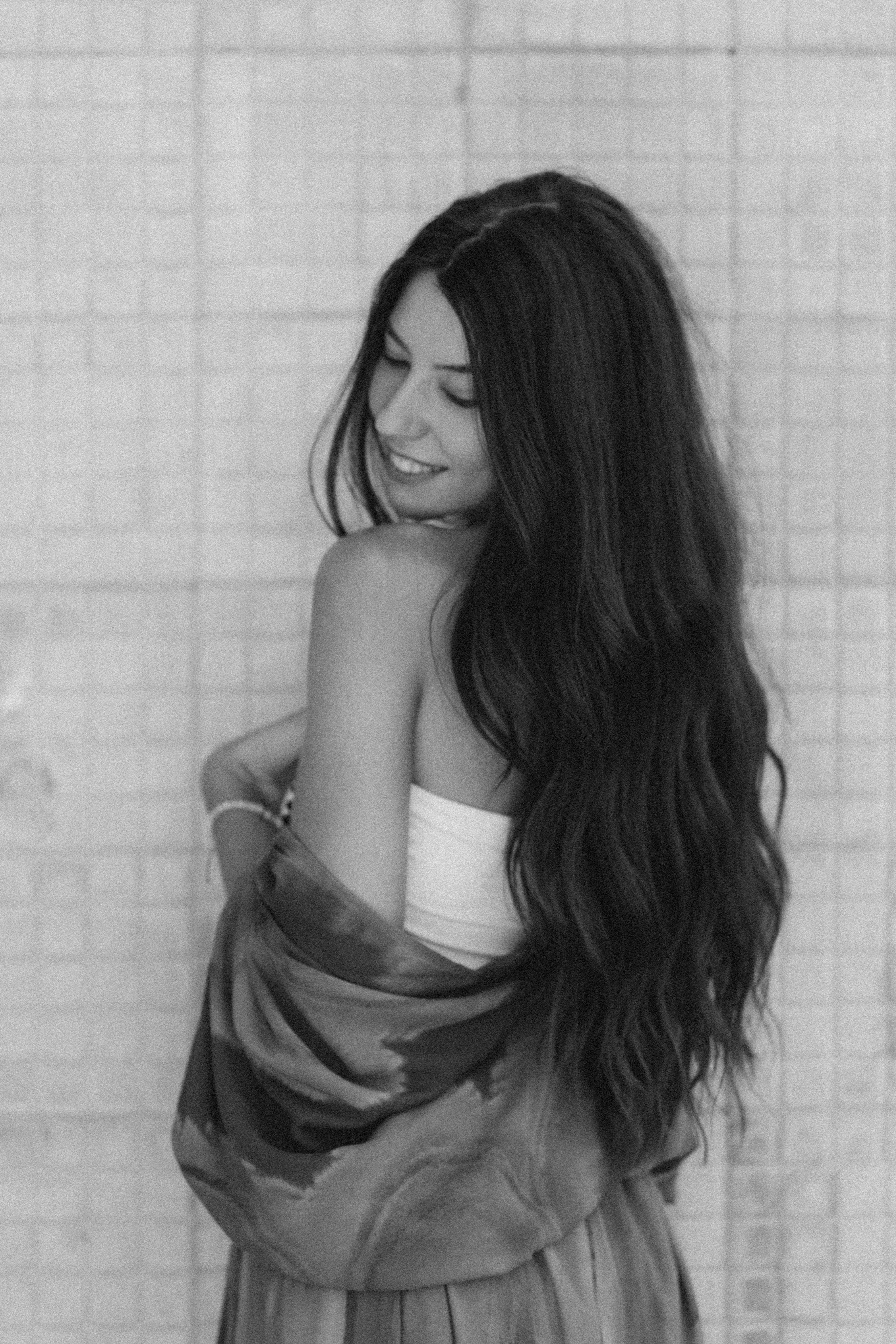 A woman with flowing hair smiles gently over her shoulder, draped in a softly colored shawl against a textured background.