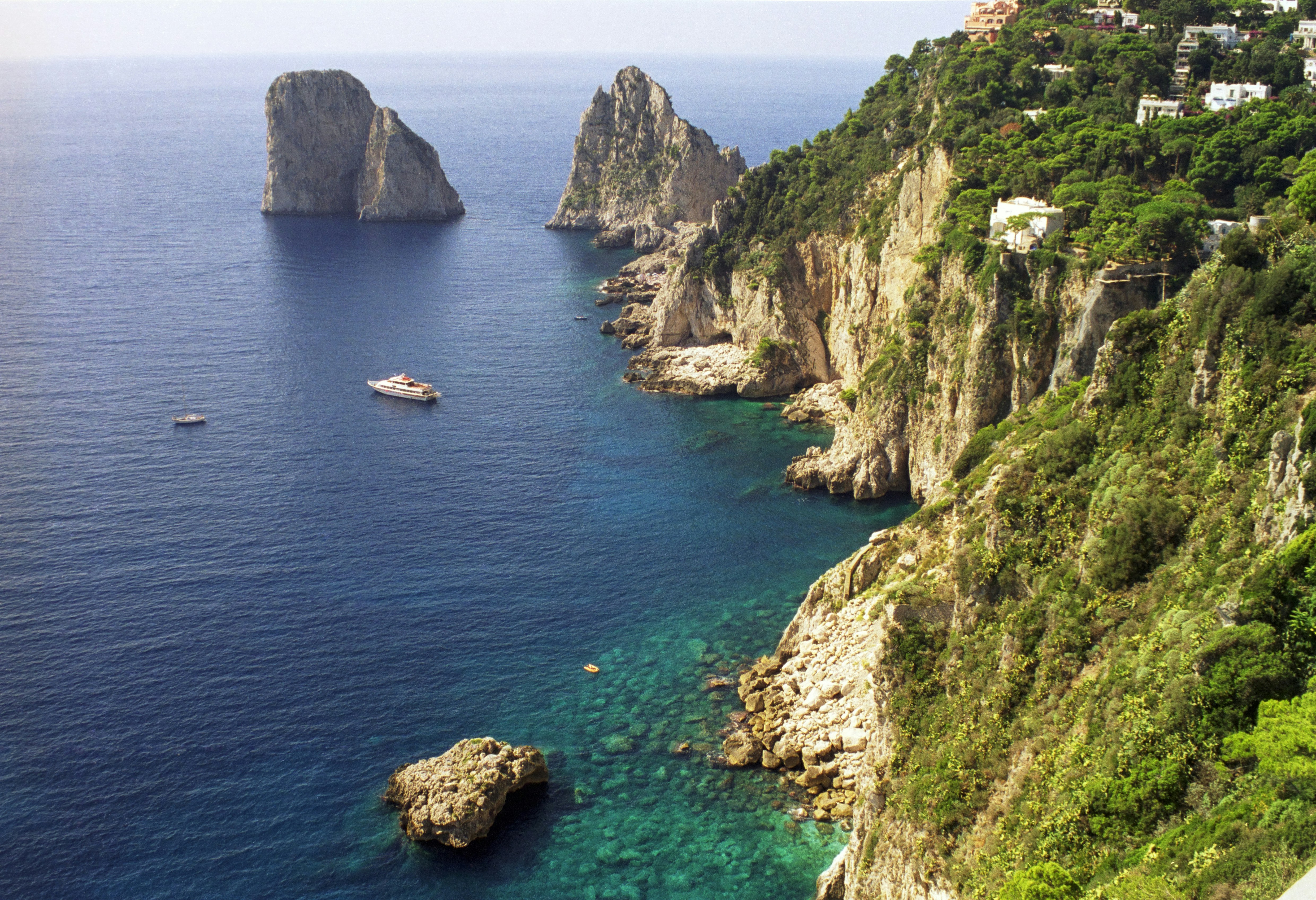 Boat navigating clear blue waters near towering coastal cliffs under a sunny sky.