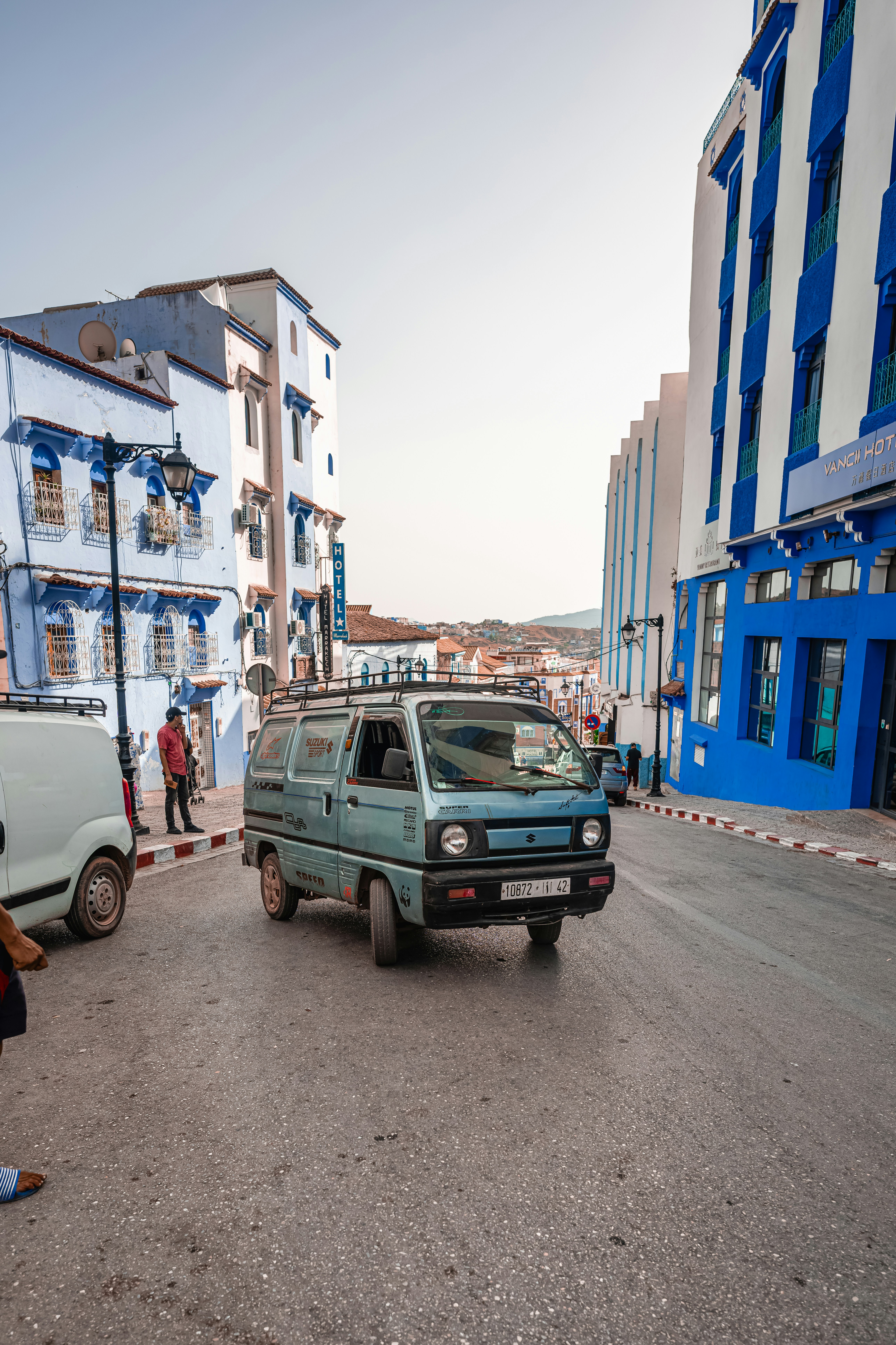 Mint Green Van Navigates a Blue-White Moroccan Street at Noon