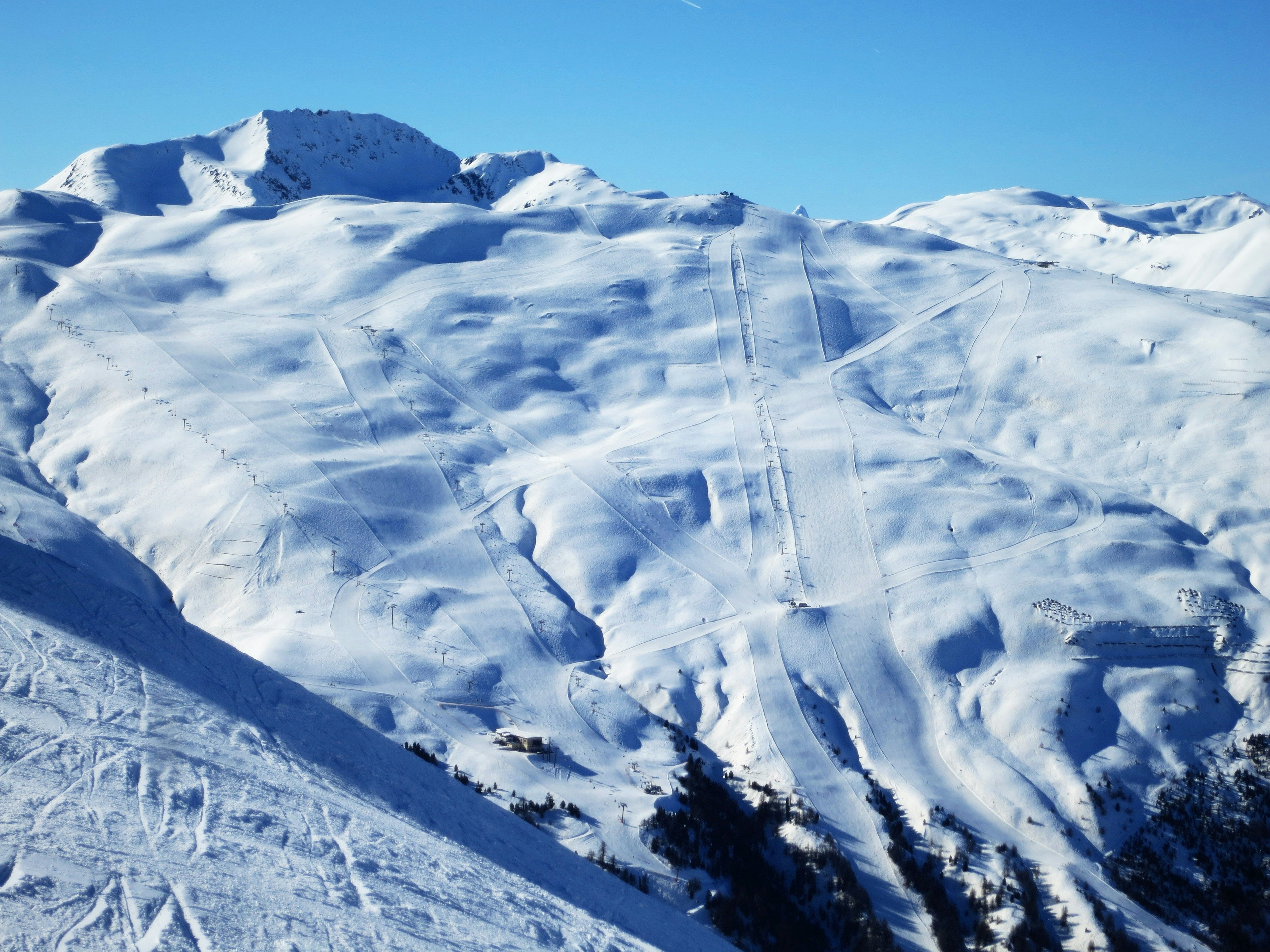Snow-covered mountain with a distant ski lift under a clear blue sky.