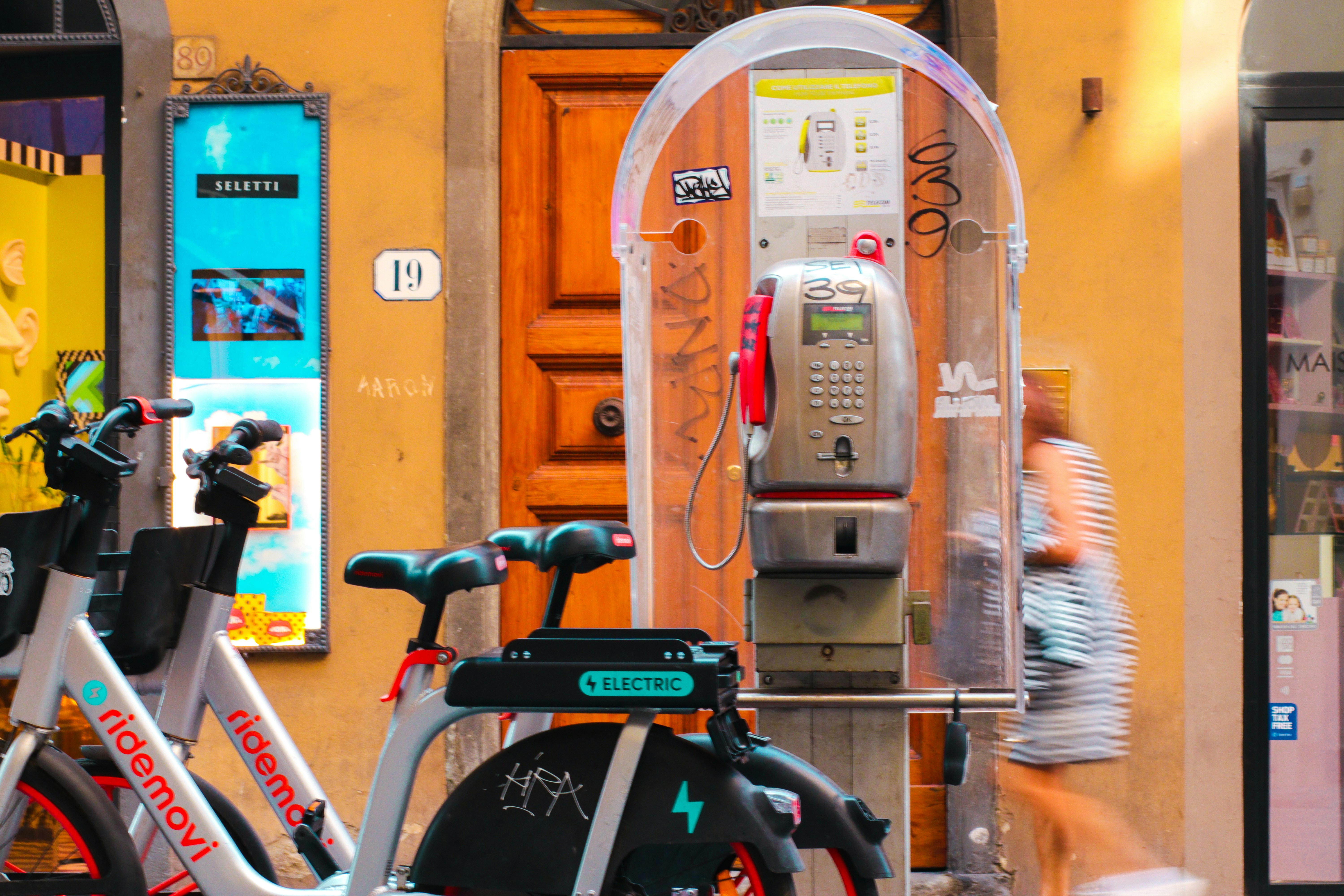 Archway of Signals: A payphone under a translucent arch amid graffiti and electric bikes