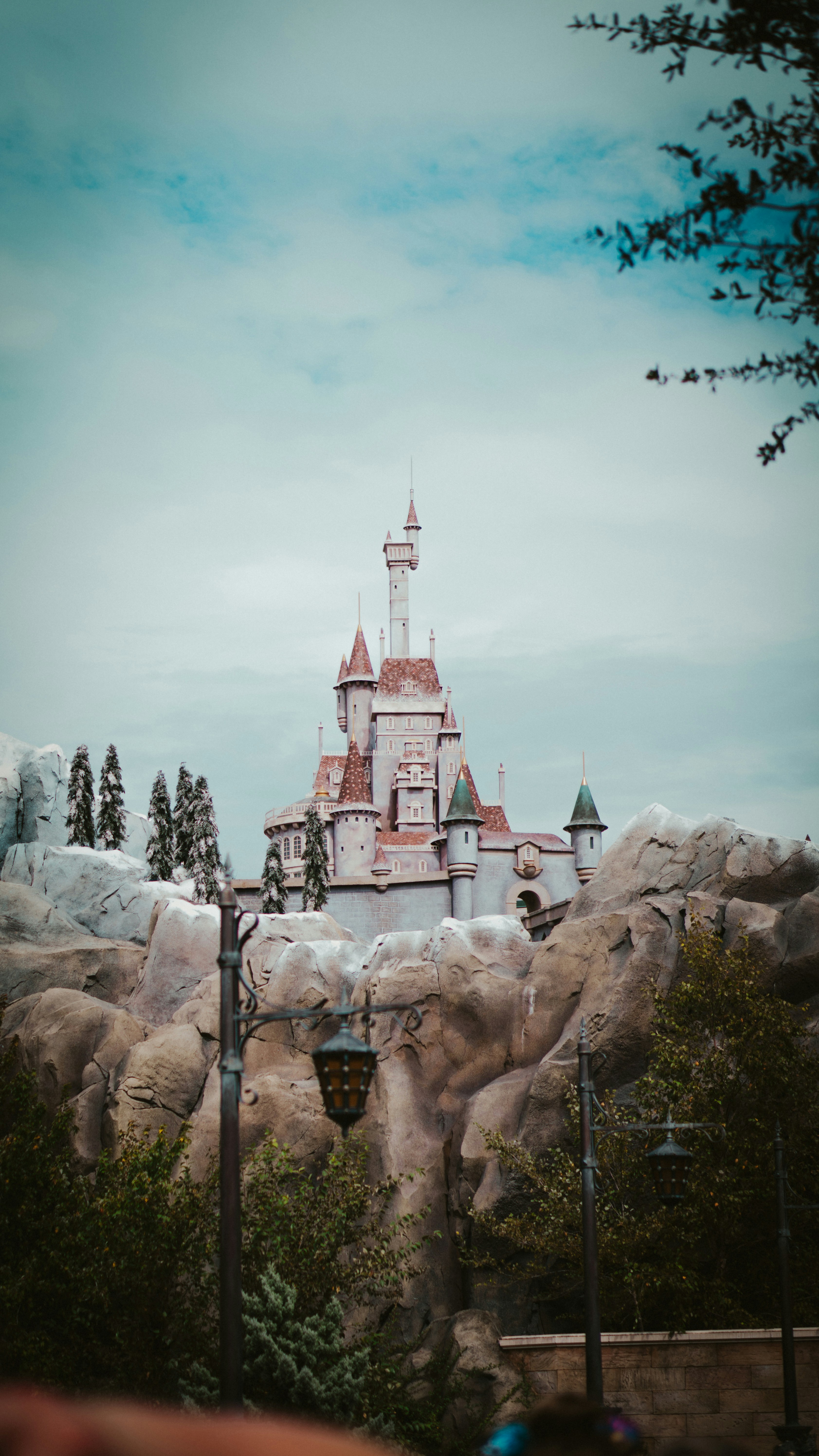 A fairy-tale castle perched on rocky terrain, surrounded by lush greenery and a cloudy sky.