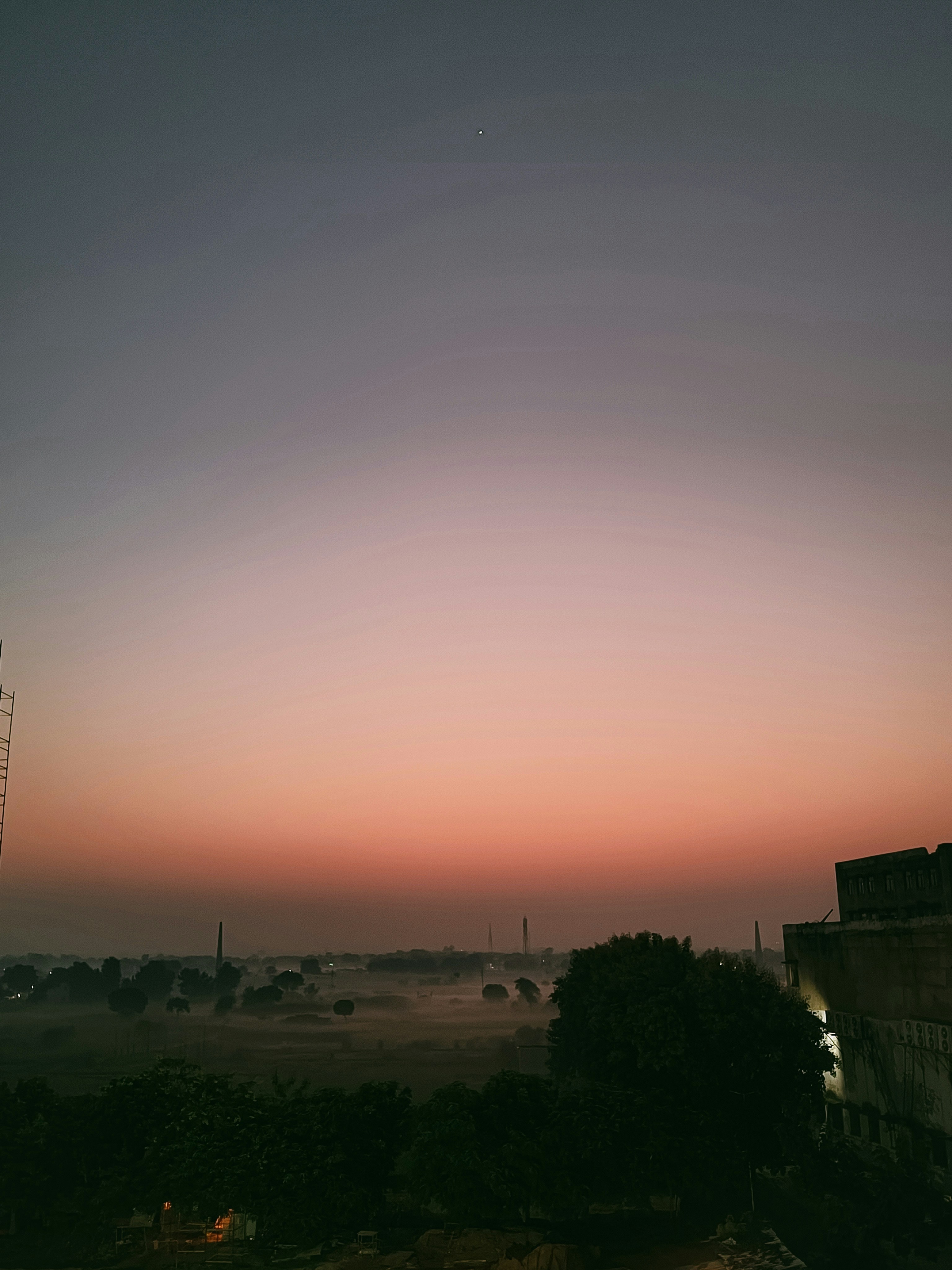 Soft peach dawn light washes over a quiet cityscape, with silhouetted trees and buildings and a faint morning mist.