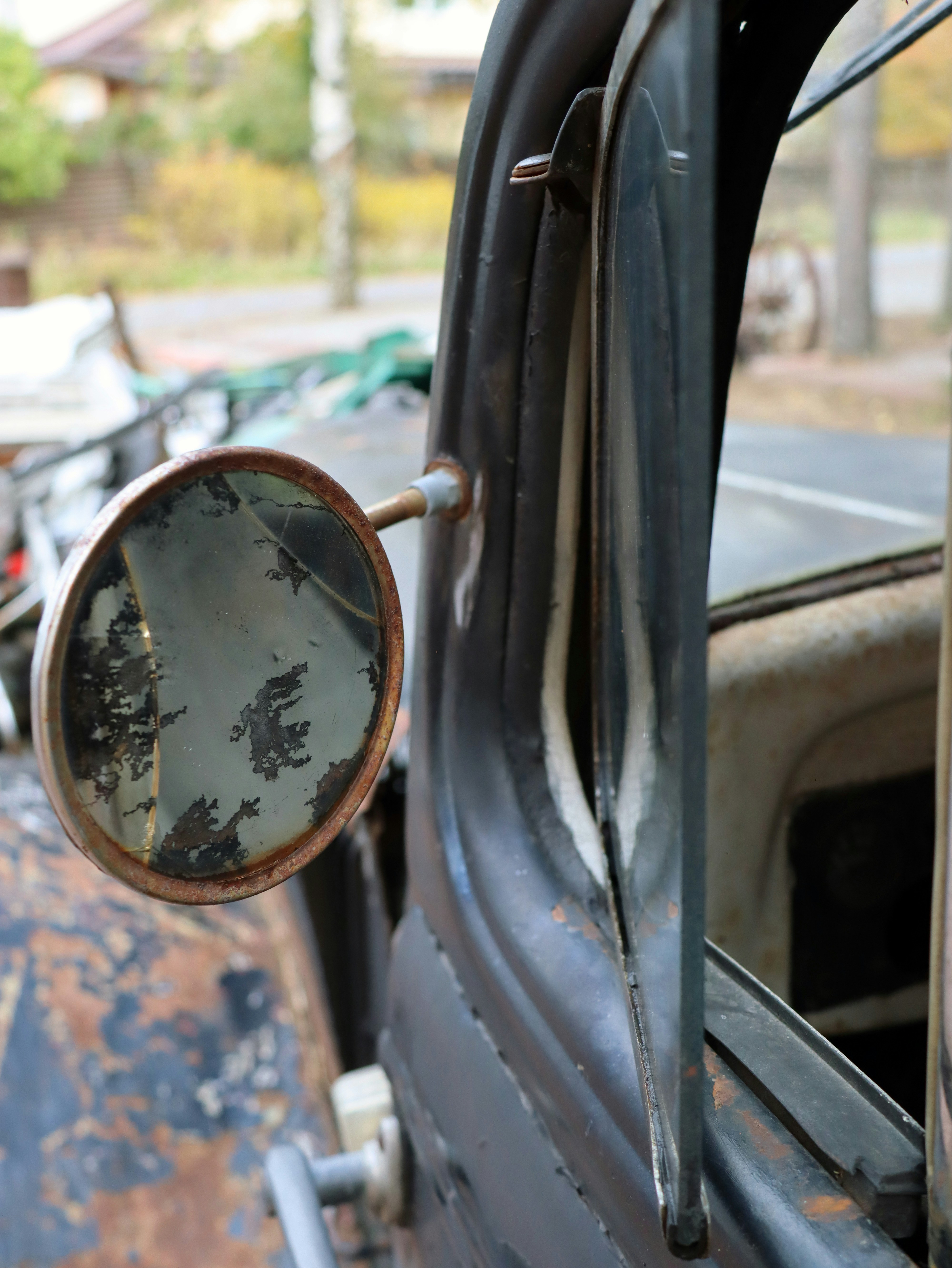 Rust and Reflection: The Weathered Side Mirror of a Quiet Junkyard Vehicle