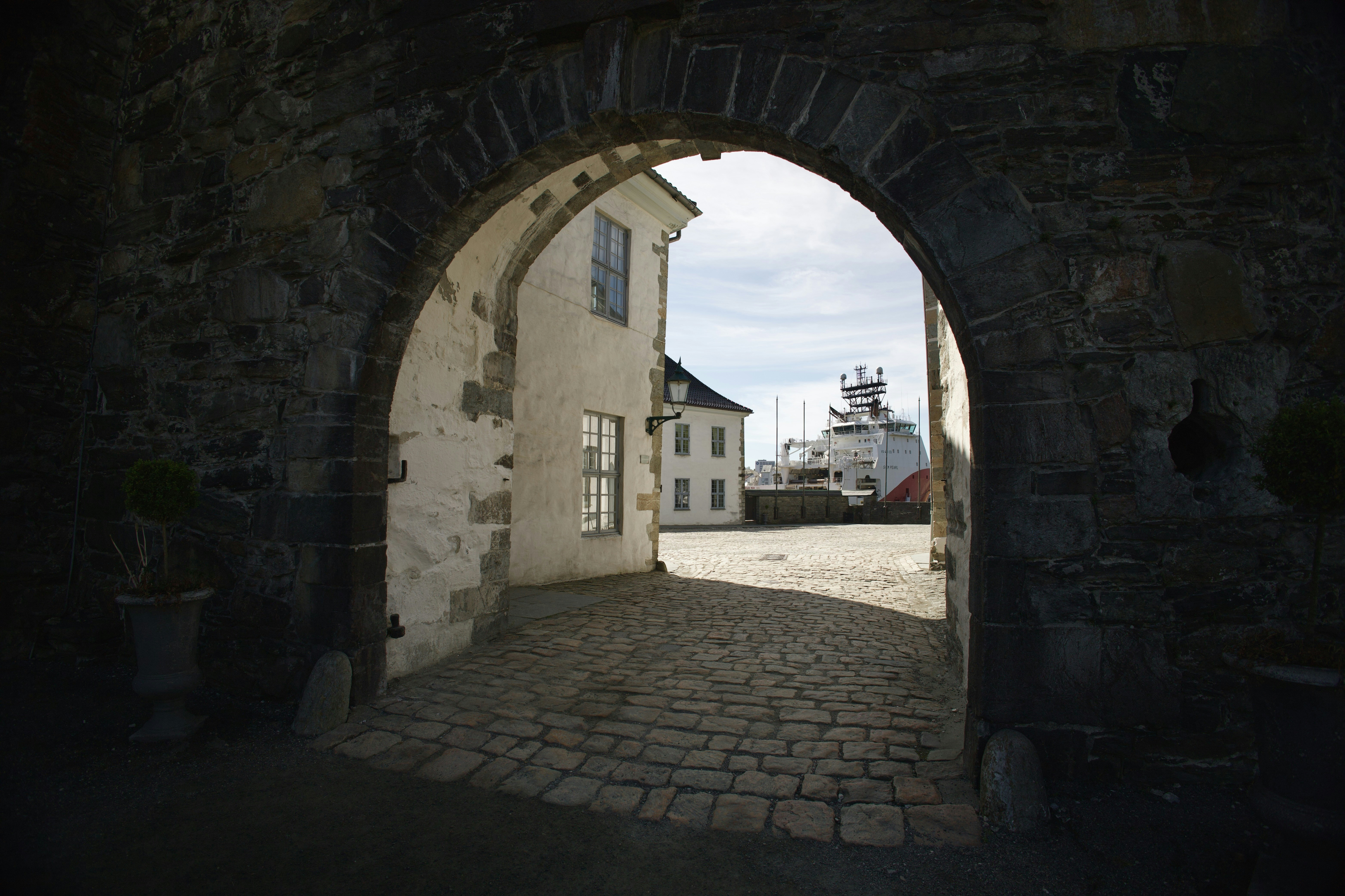 Archway to a Maritime Courtyard: Cobblestones, White Facades, and Distant Ships
