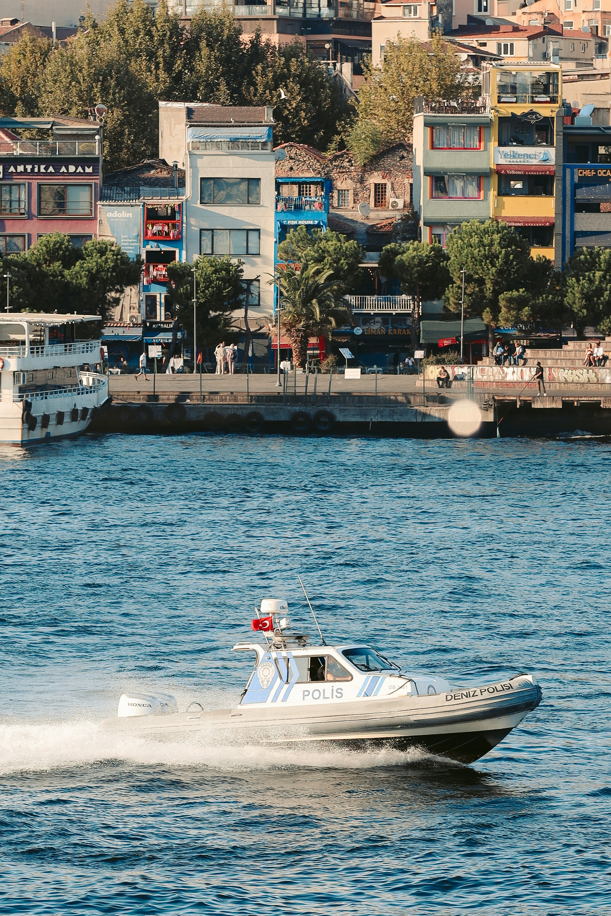 Blue Wake, Colorful Shoreline: A Police Boat Speeds by a Turkish Waterfront