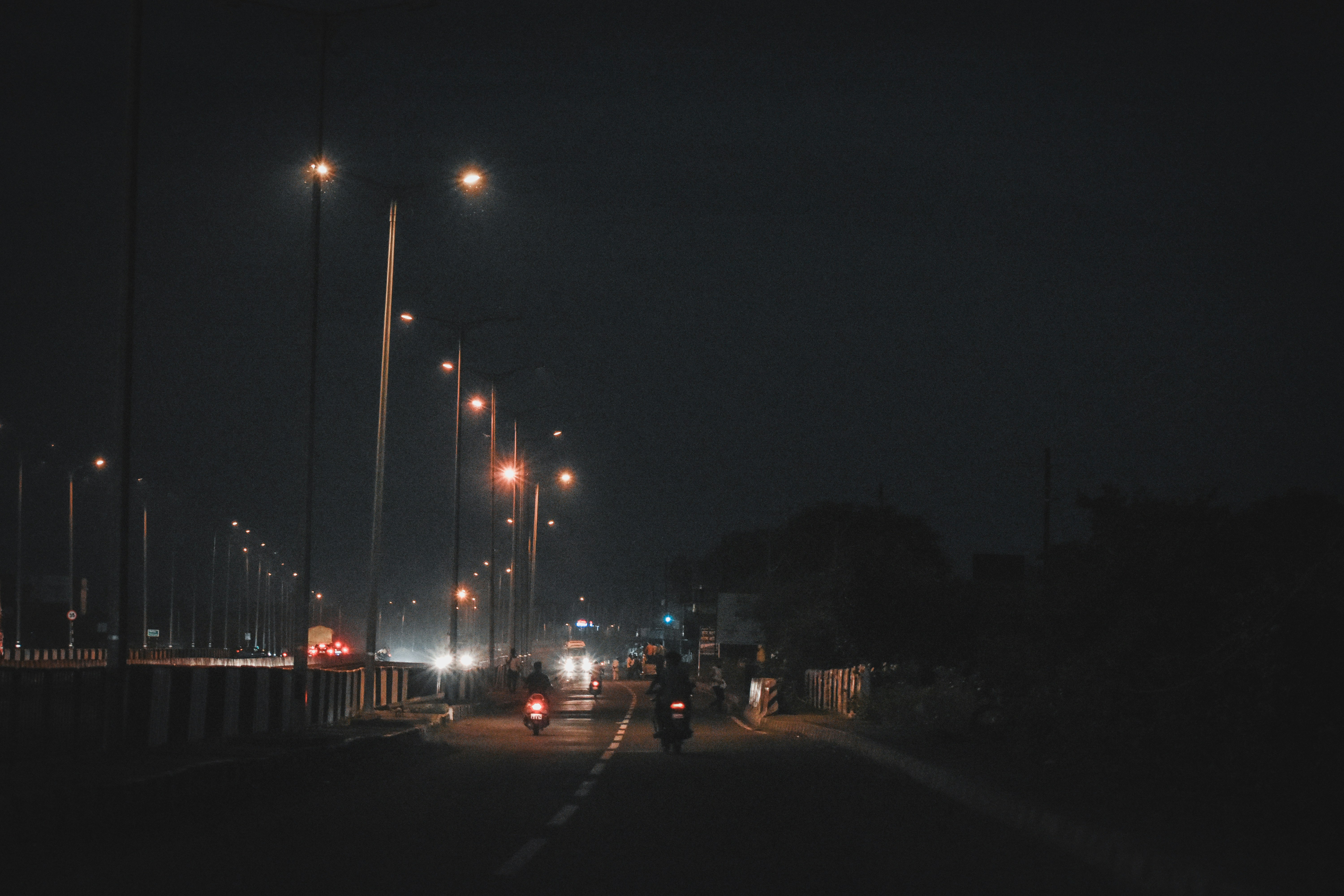 A quiet road at night illuminated by streetlights, with motorcycles navigating the path ahead. The scene captures the essence of urban life after dark.