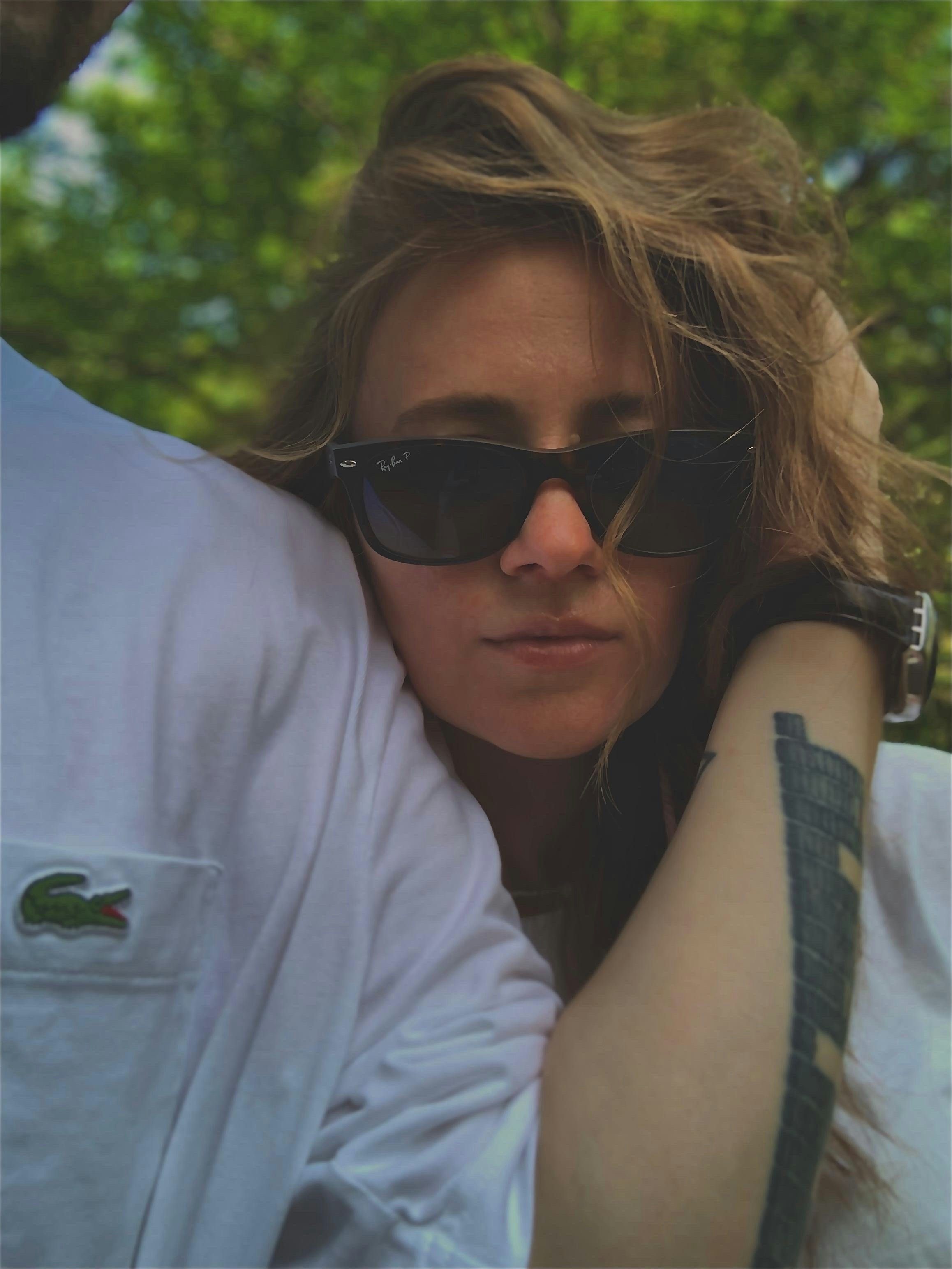 Under the Green Canopy: A Wind-Swept Portrait in Sunglasses