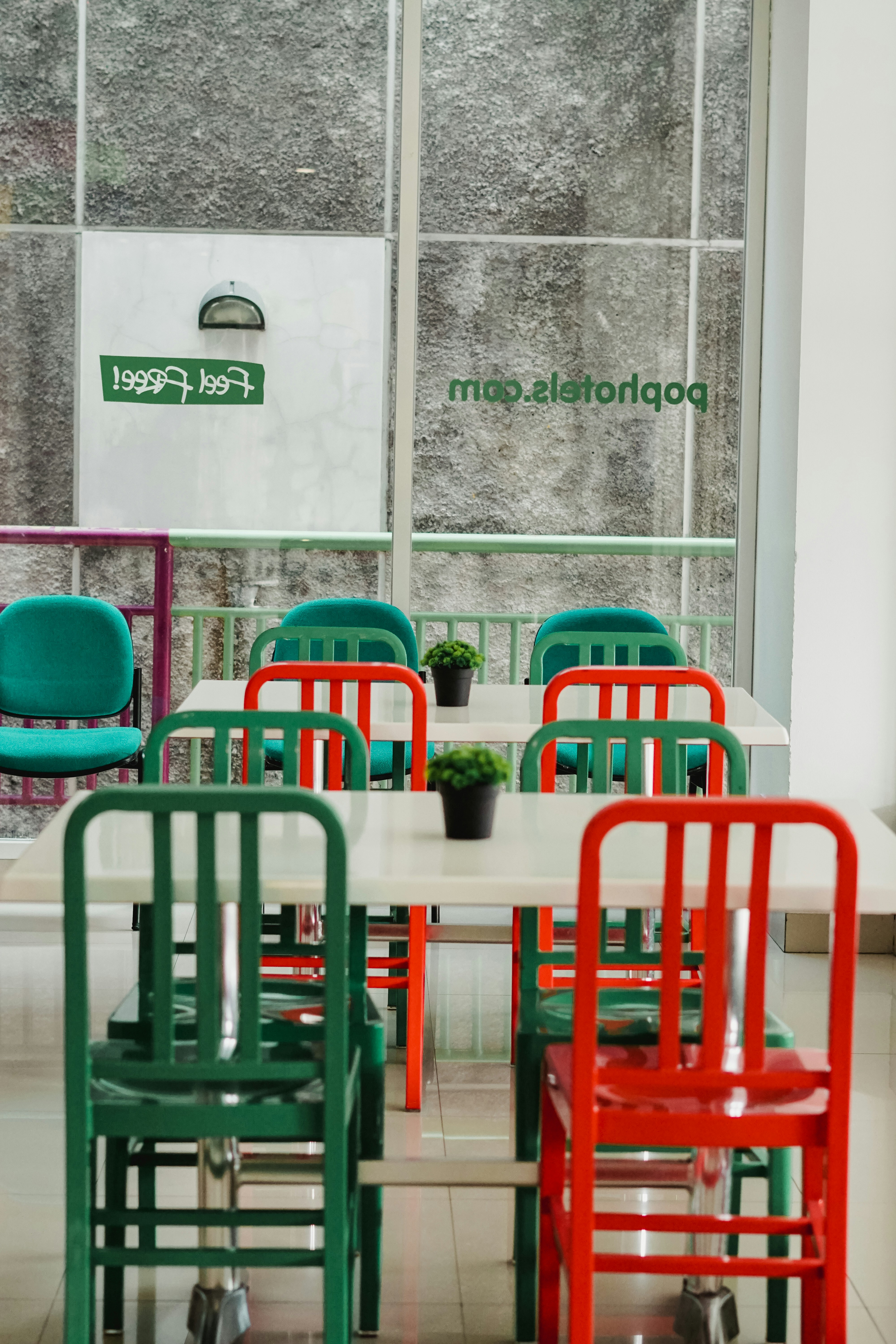 Chromatic Café Grid: Emerald, Teal, and Crimson Chairs Framing a Quiet Table Corridor