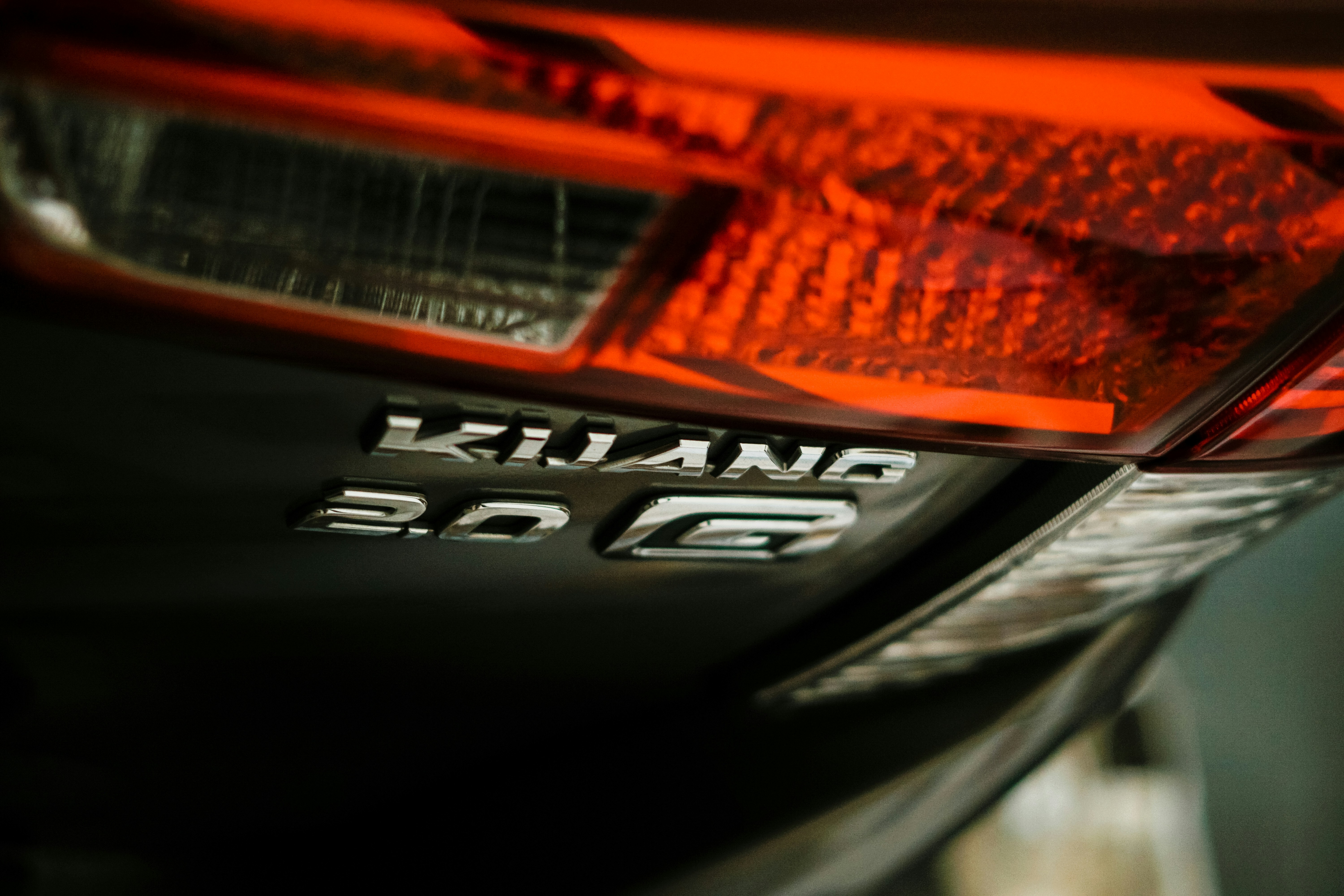 Crimson Taillight Glow Framing a Chrome Emblem on a Dark Car Rear