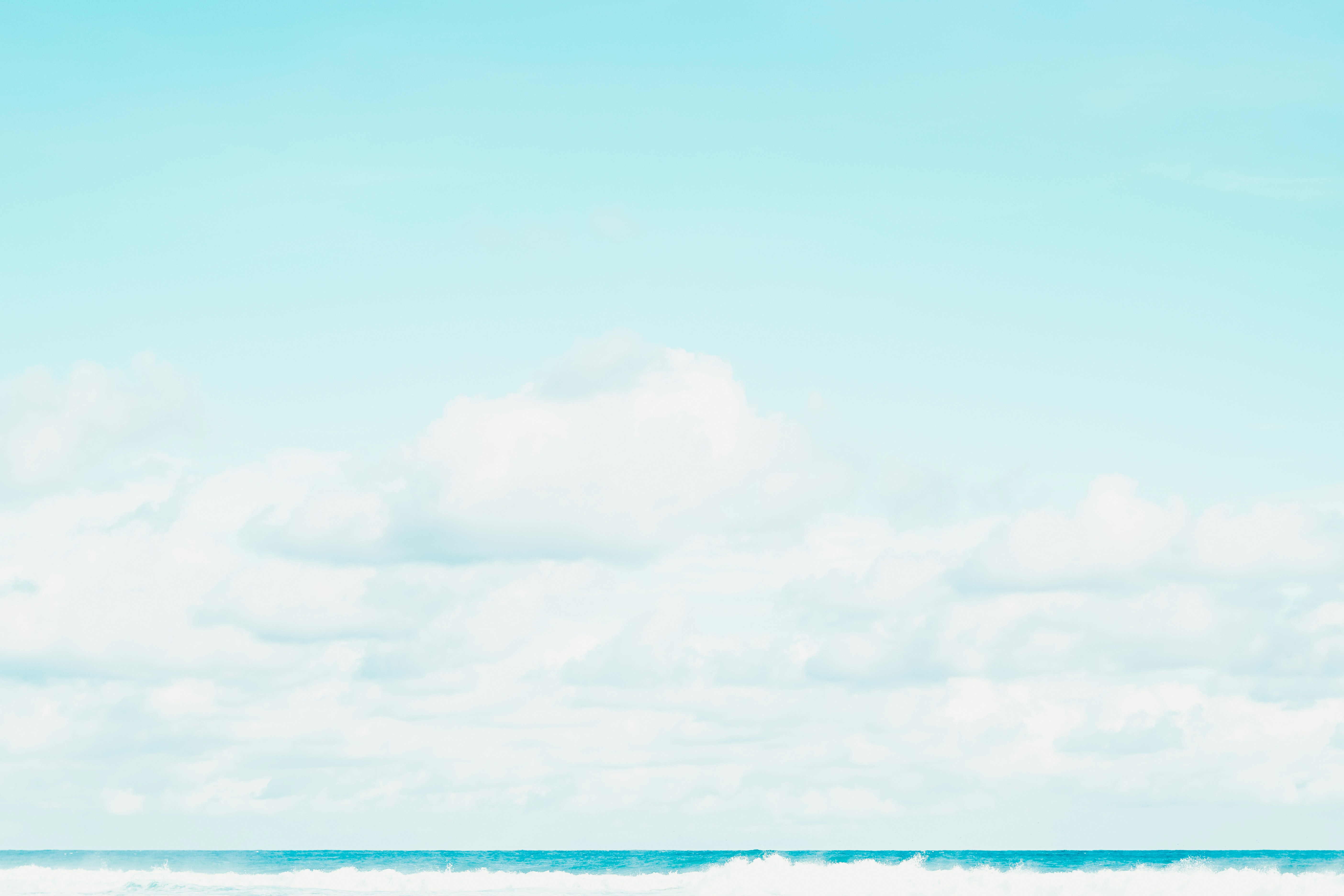 Gentle waves lapping against the shore under a soft blue sky dotted with clouds.