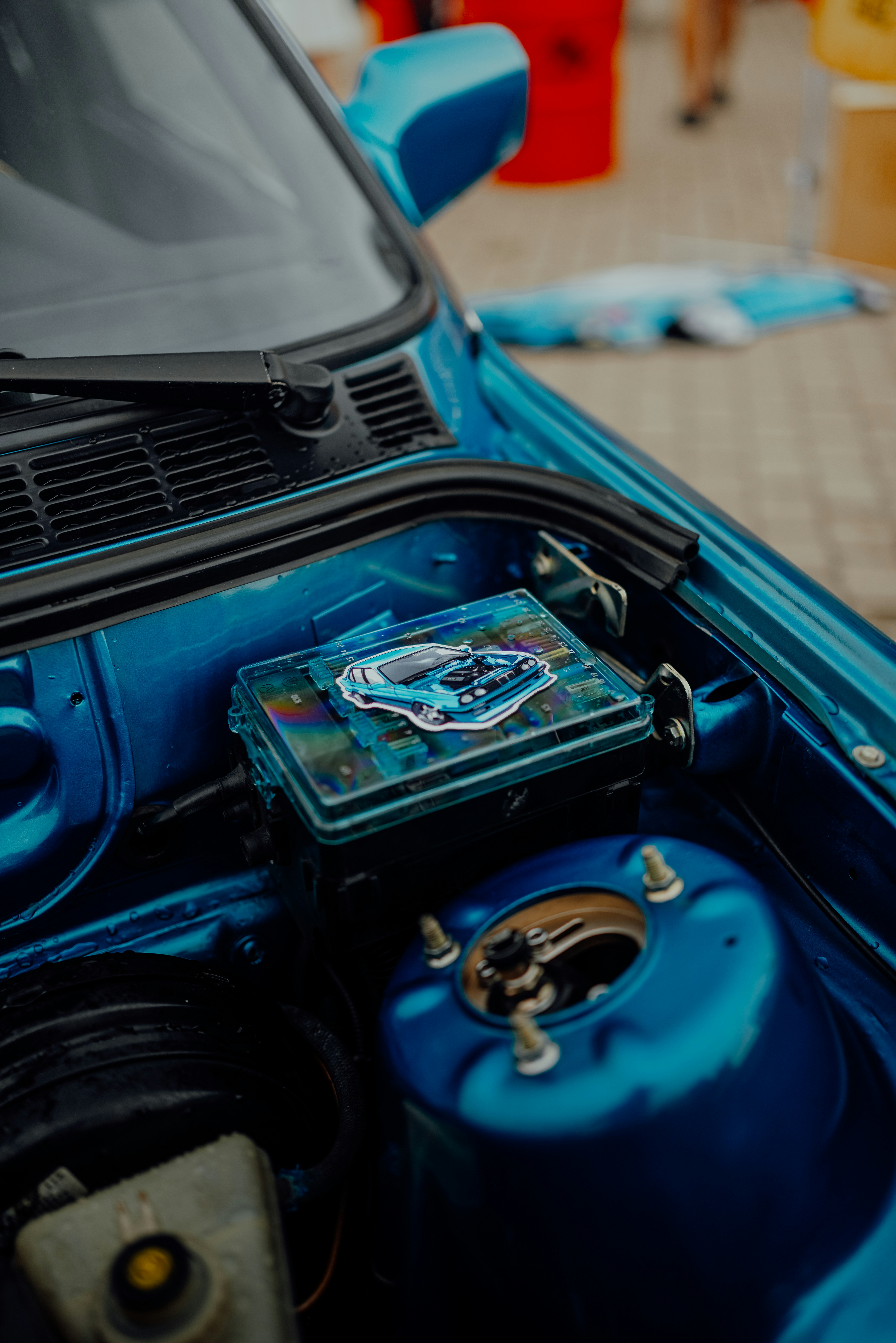 Under the Blue Hood: A Clear Case Holds a Retro Car Emblem in a Gleaming Engine Bay