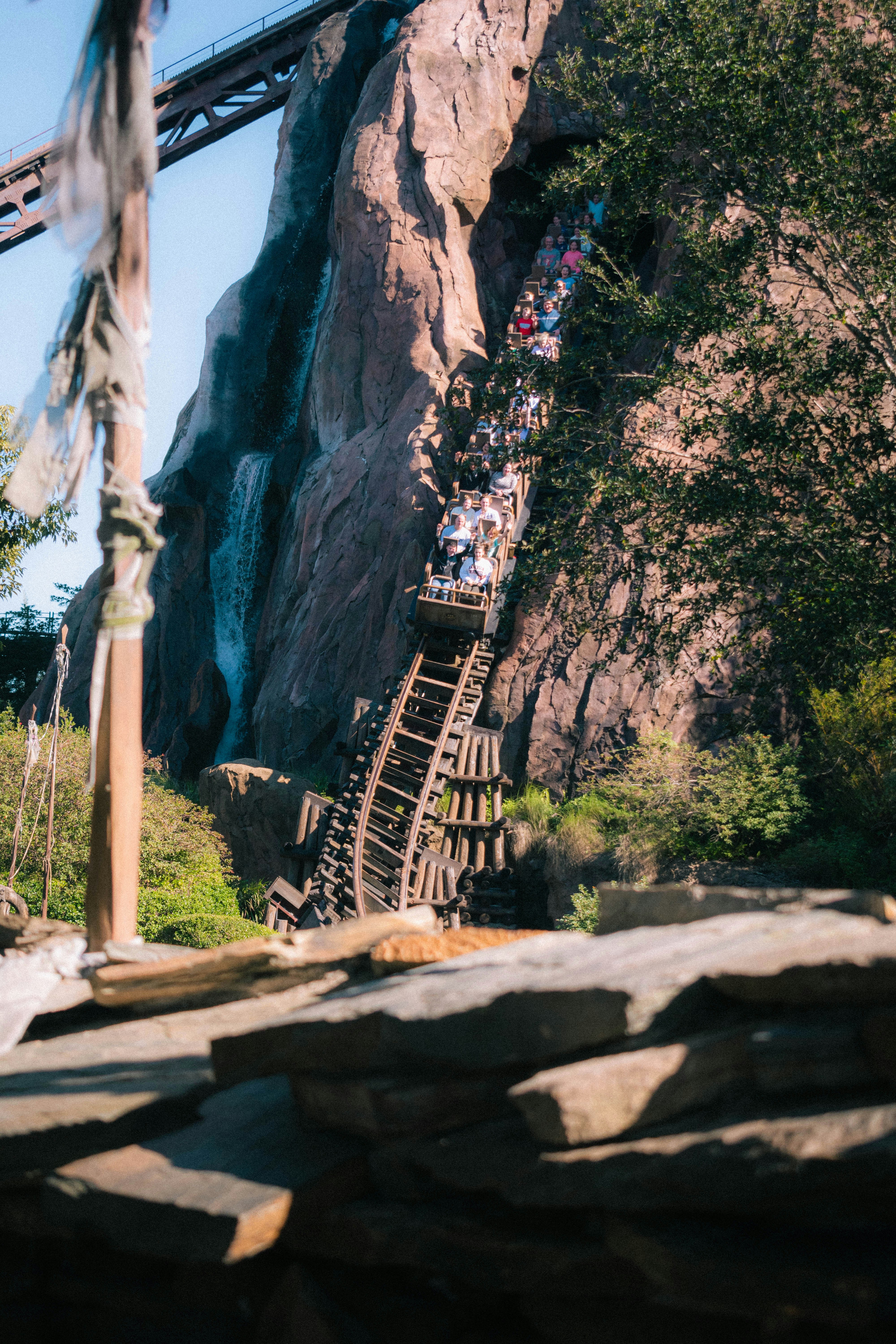 Cliffside Timber Coaster: Riders Descend a Sunlit Rock Face