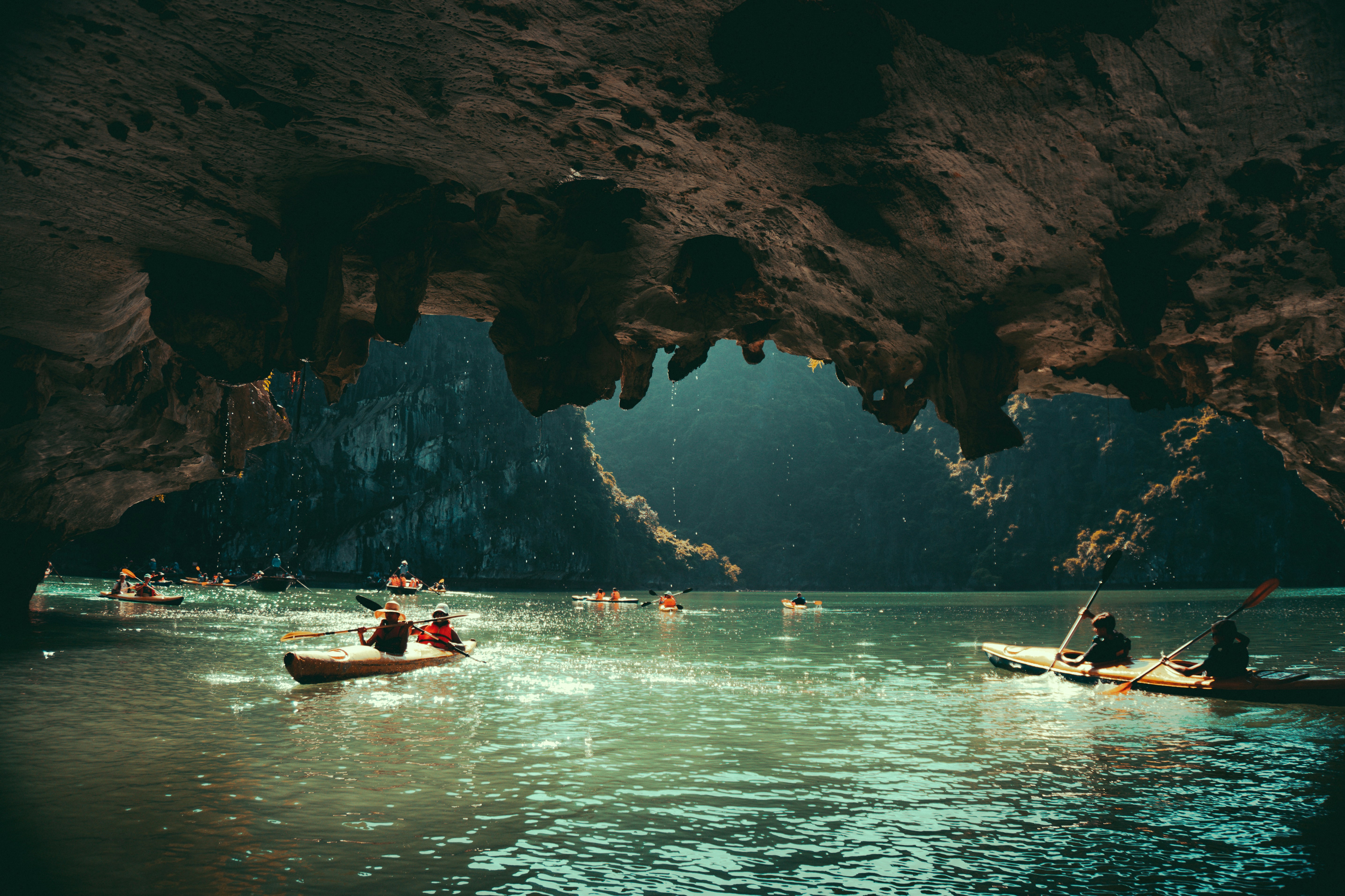 Canoes navigate through a sunlit cave with sparkling waters and rugged rock formations.