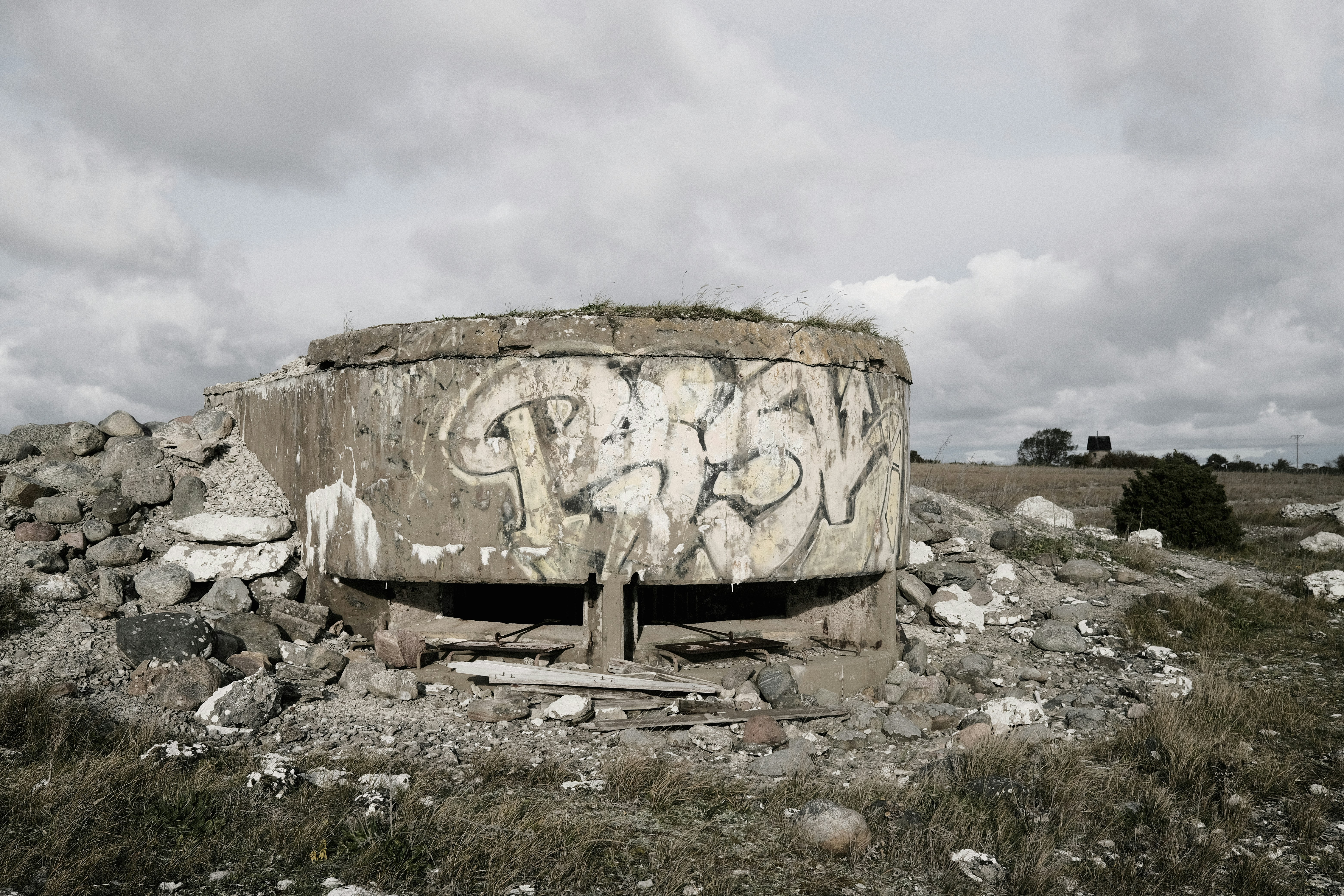 An abandoned bunker in the eastern of Gotland, Sweden. The concrete structure has been painted with grafitti over the years and has been weathered down. | a concrete structure with graffiti on it in a field