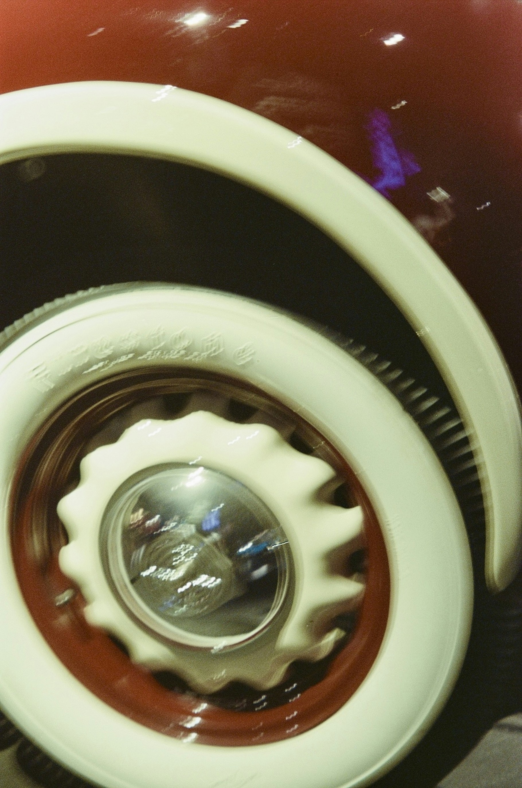 Close-up photograph of a vintage whitewall tire with a gear-like center hub. Warm lighting and reflections emphasize the wheel's retro design.