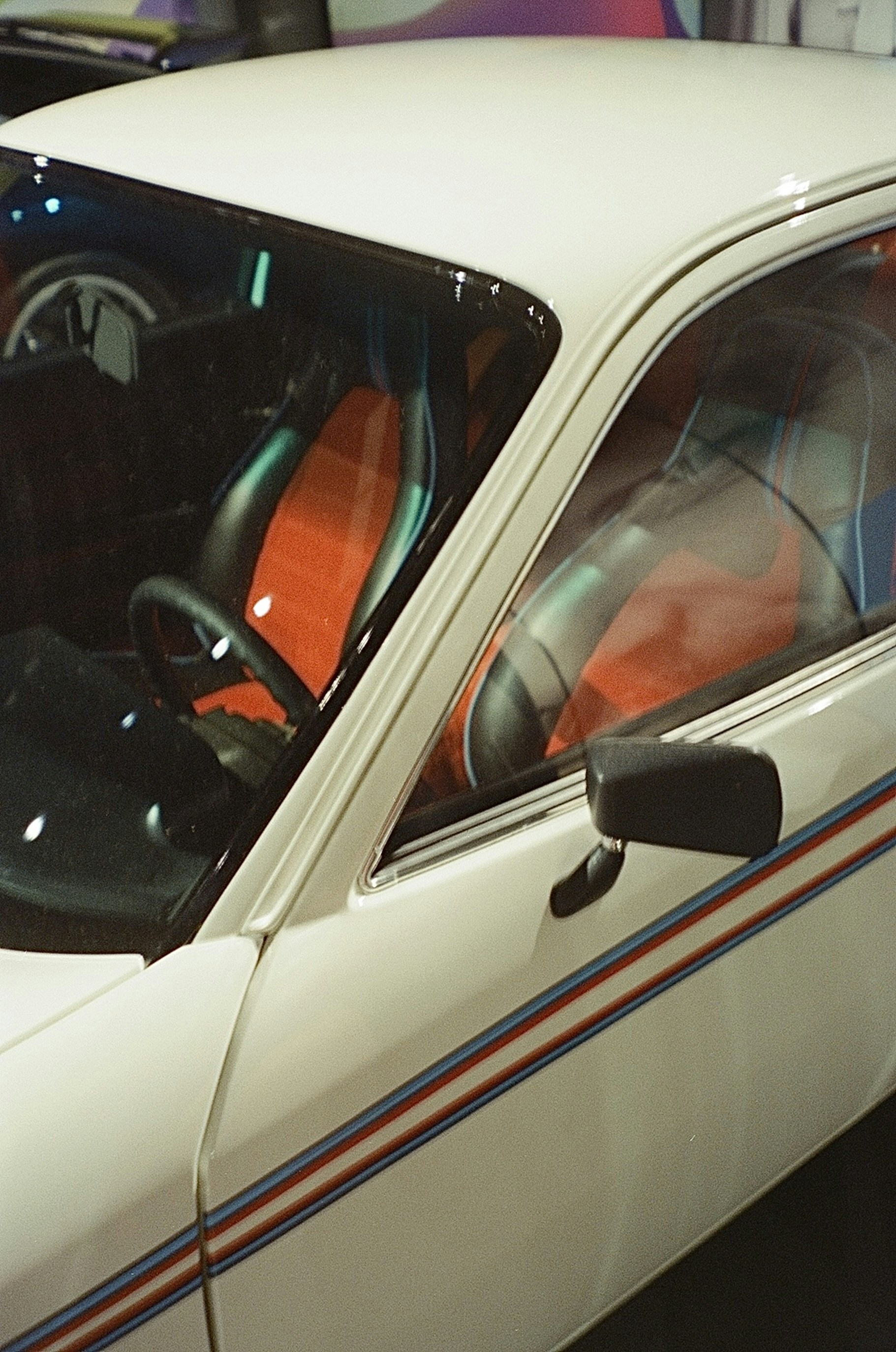 Close-up of a white vintage car door with orange interior seats visible through the window.