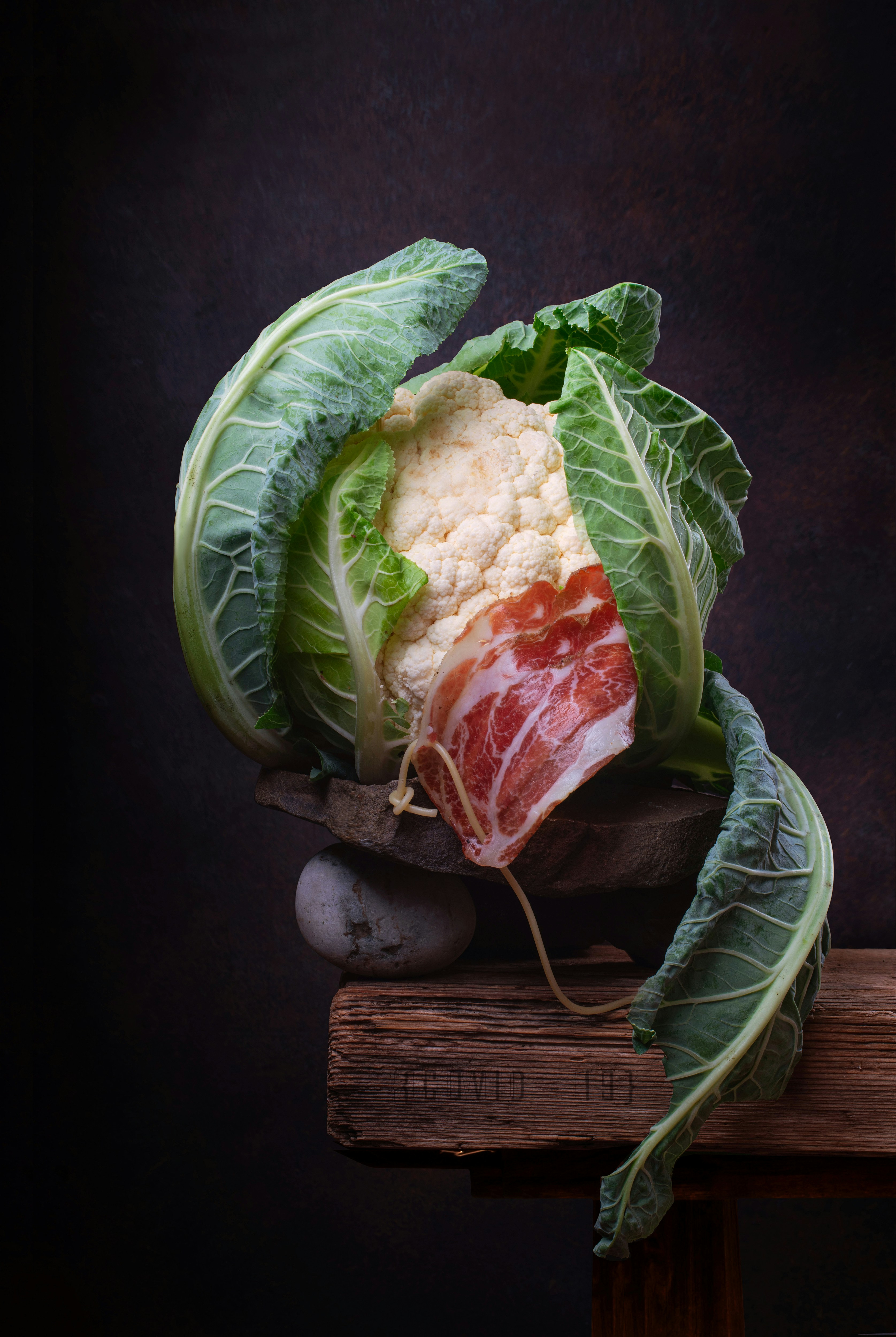A vibrant arrangement of a cabbage and cauliflower, complemented by a slice of cured meat, showcasing a harmonious blend of natural elements and culinary art.
