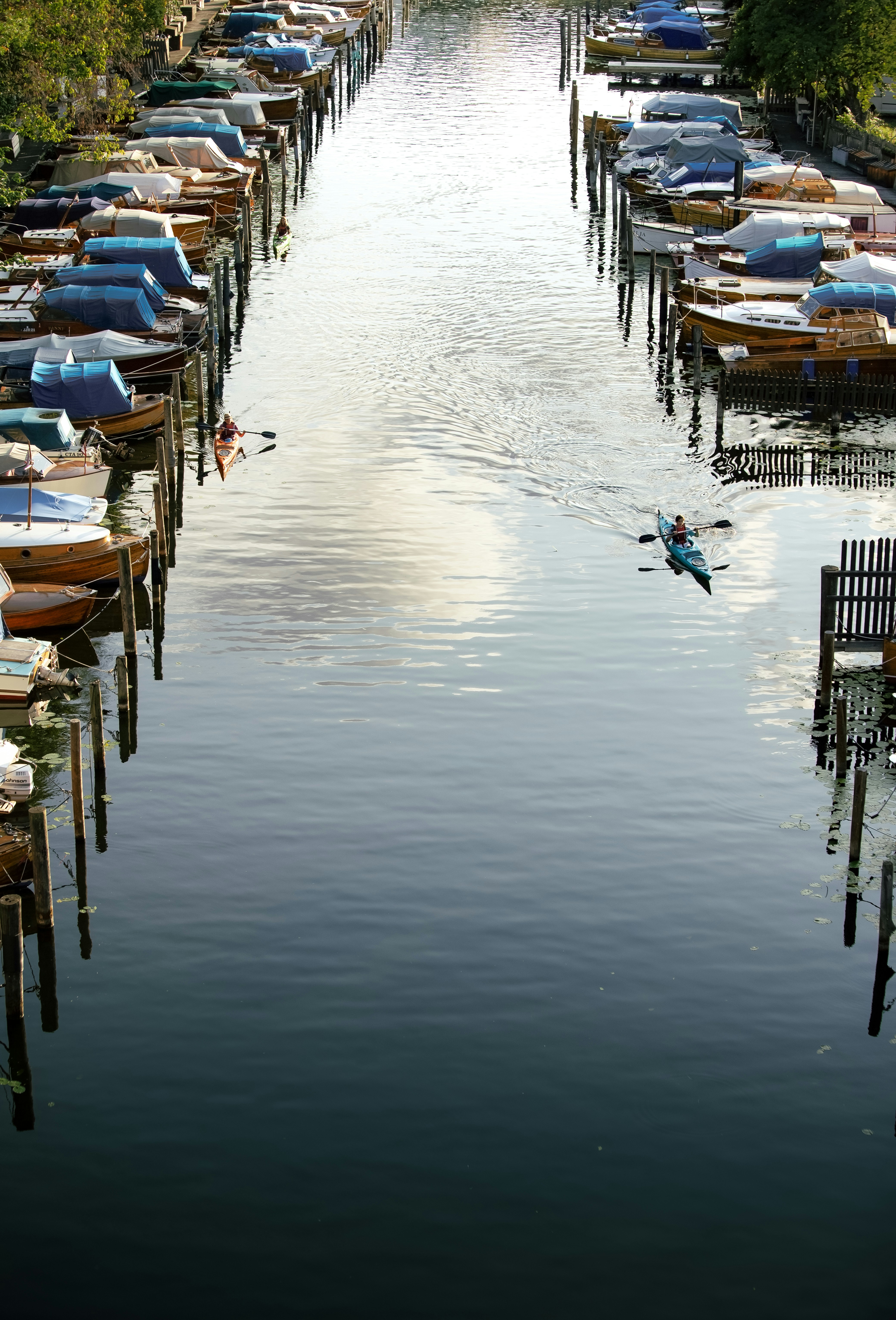 Dockside Reverie: Kayaks Thread a Narrow Canal Between Moored Boats
