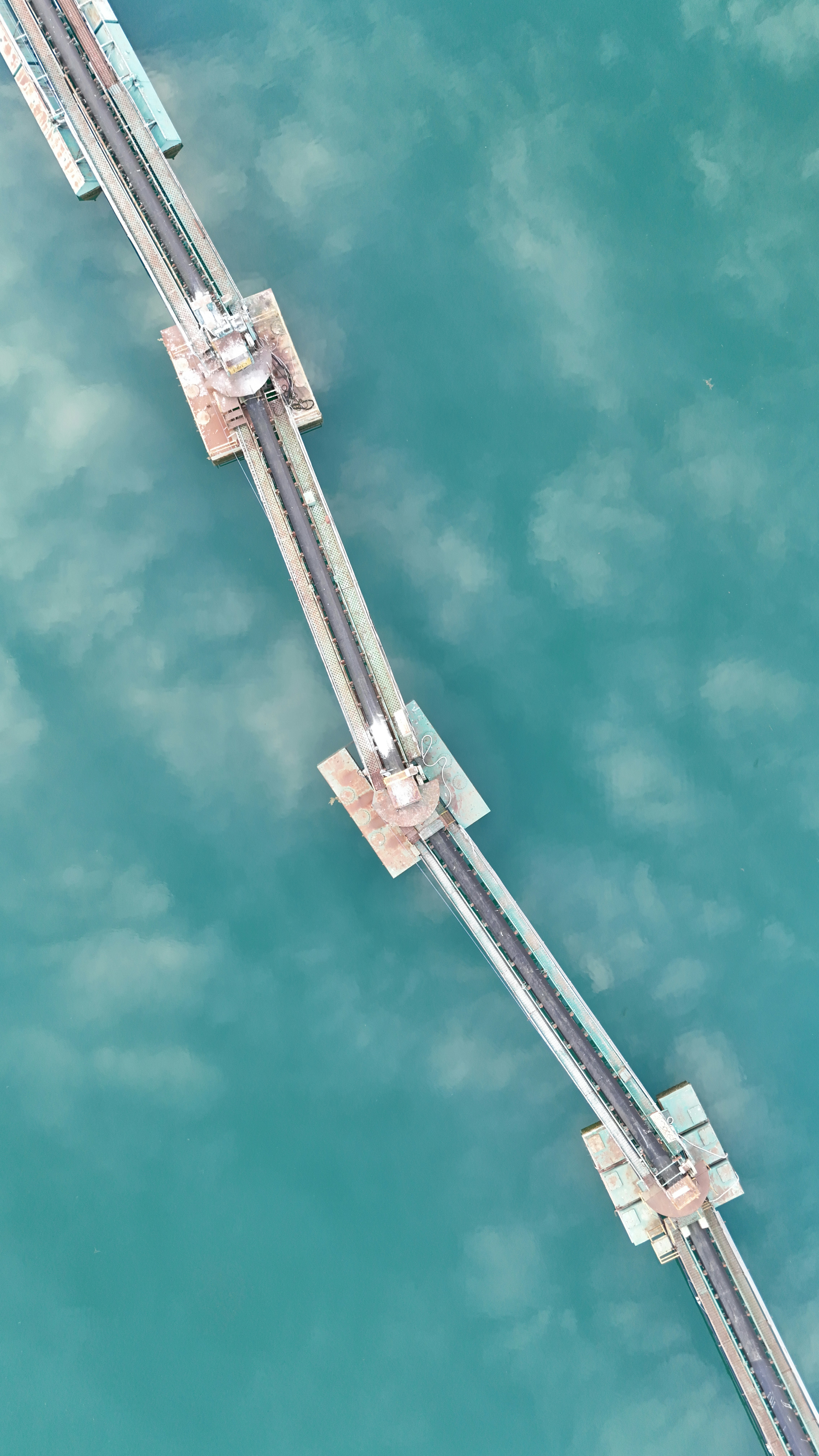 Aerial photograph of a bridge crossing turquoise water, viewed from above along a diagonal span.