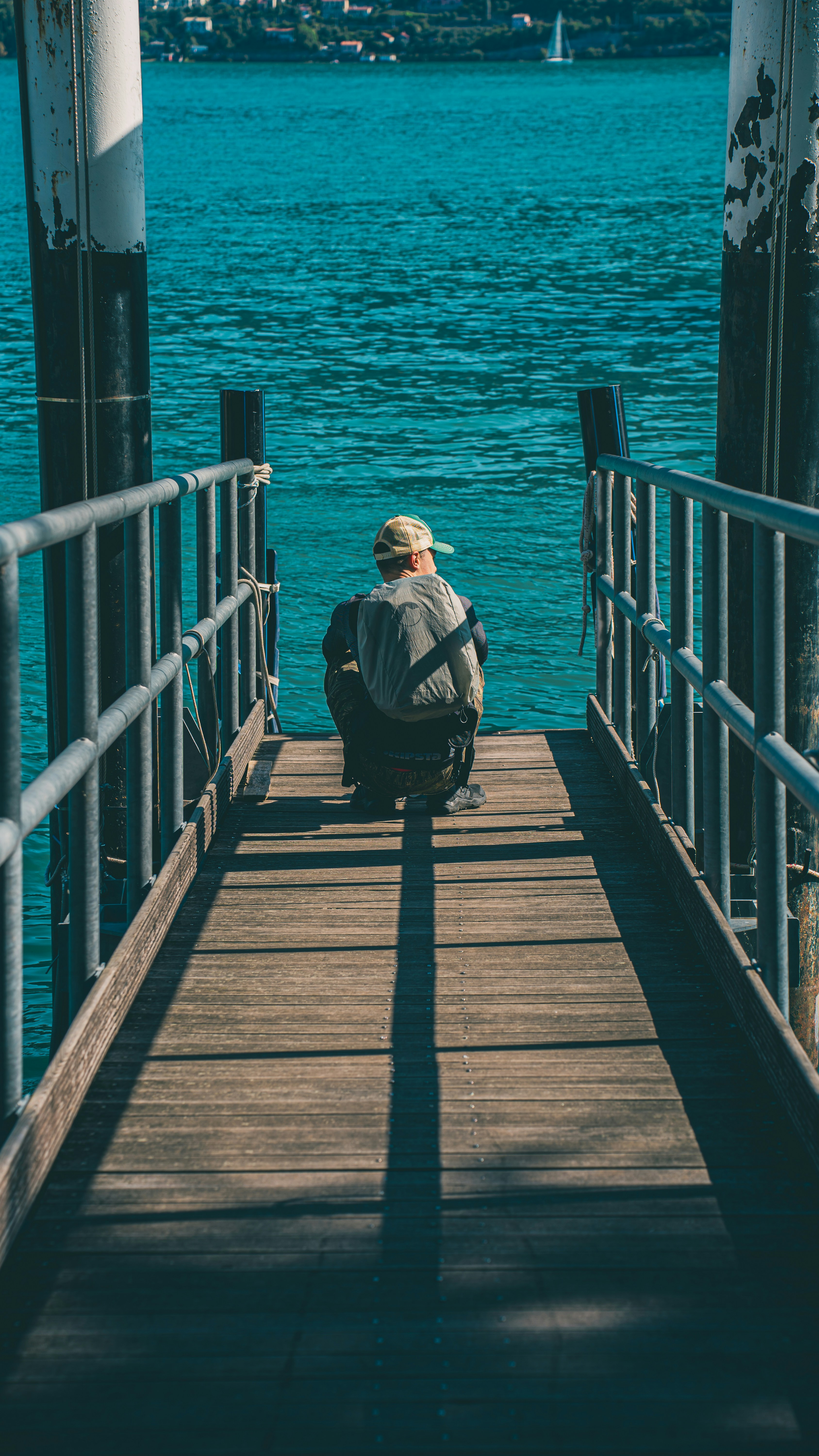 A man sitting on a dock looking out at the water photo – Free Water ...