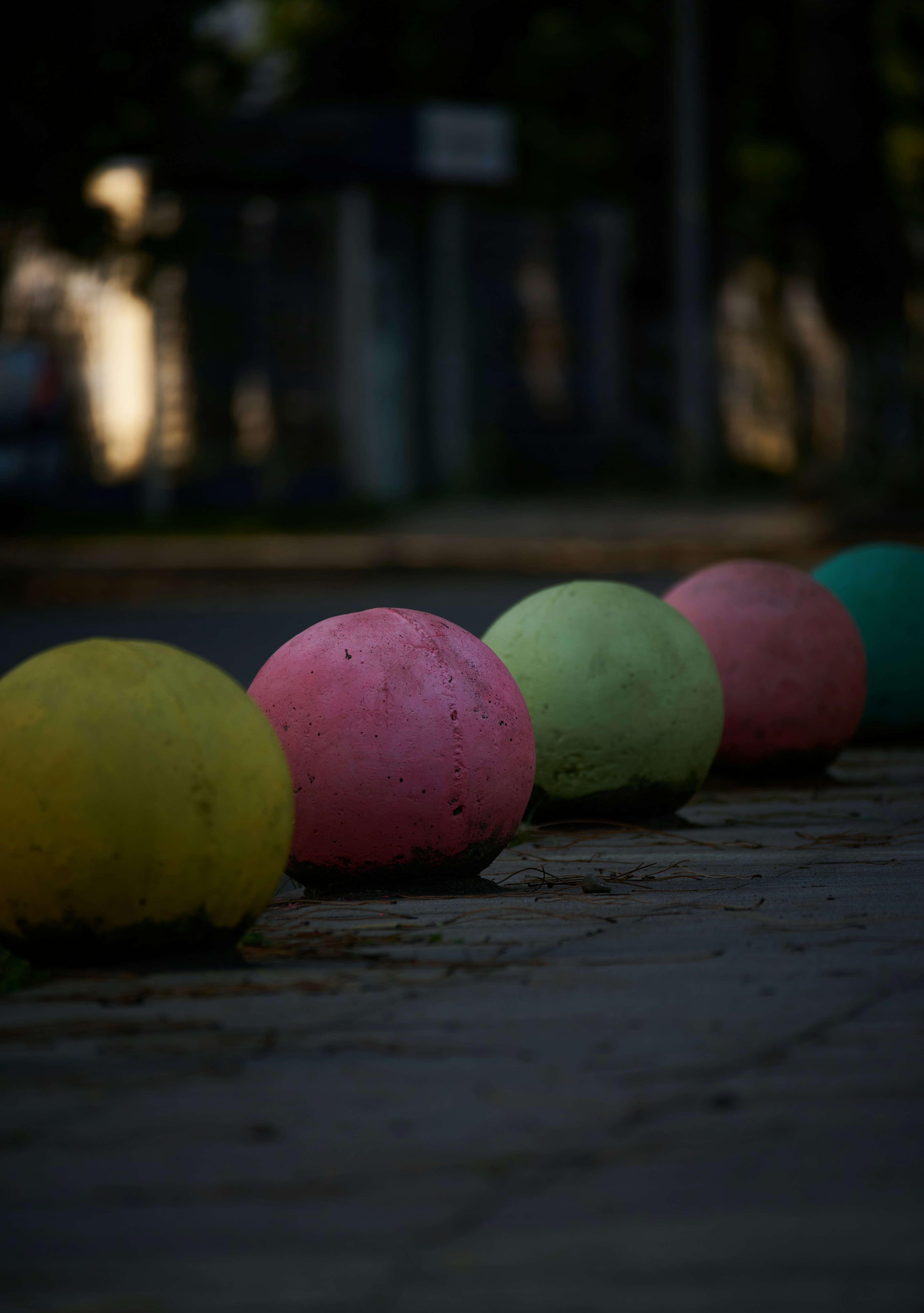 Vibrant, rounded barriers in shades of yellow, pink, green, and blue line a pavement, casting soft shadows in the evening light.