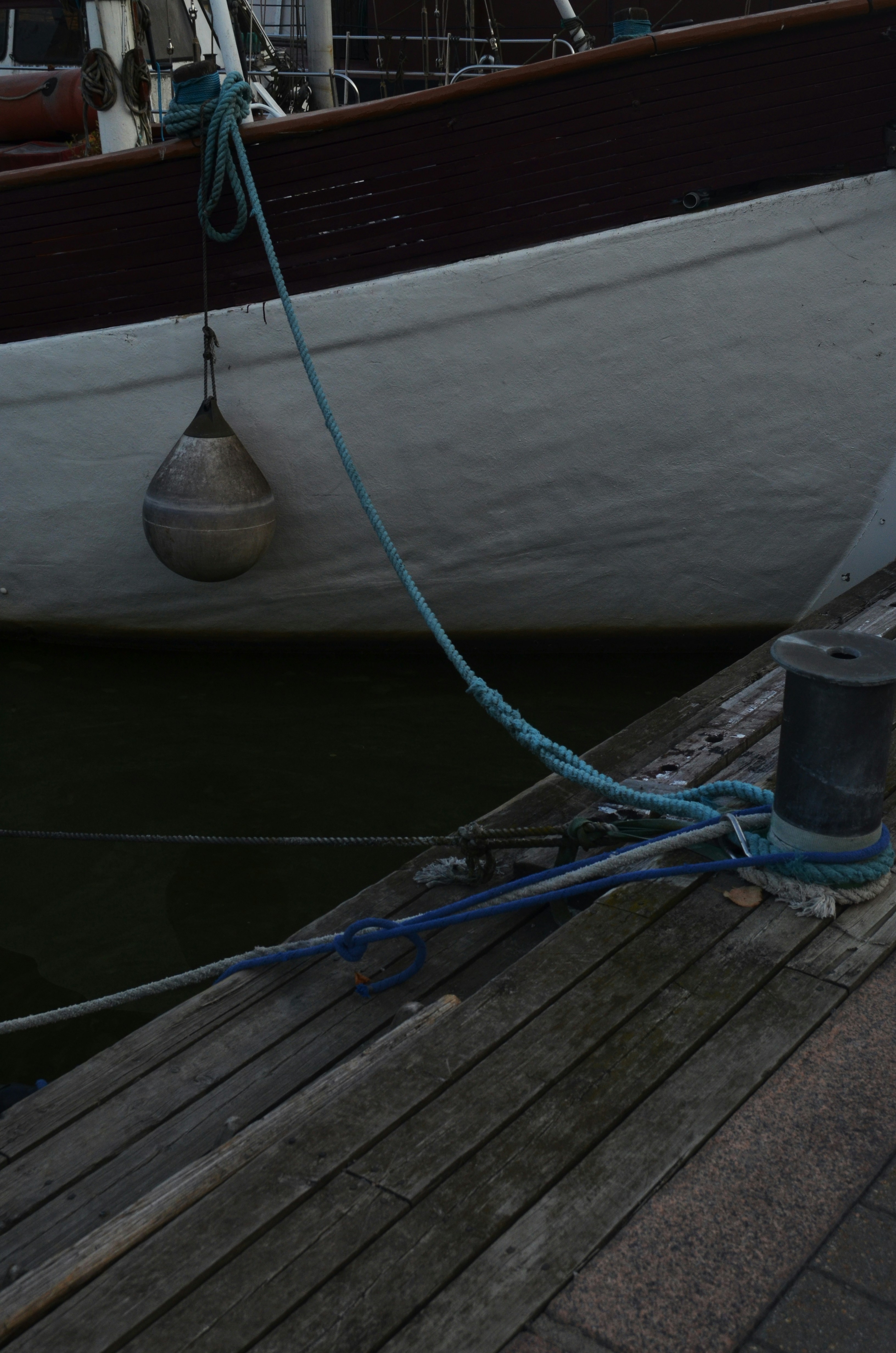 A buoy hangs from a rope next to a moored boat, with textured wooden planks forming the dock. The scene evokes a sense of calm in a maritime setting.