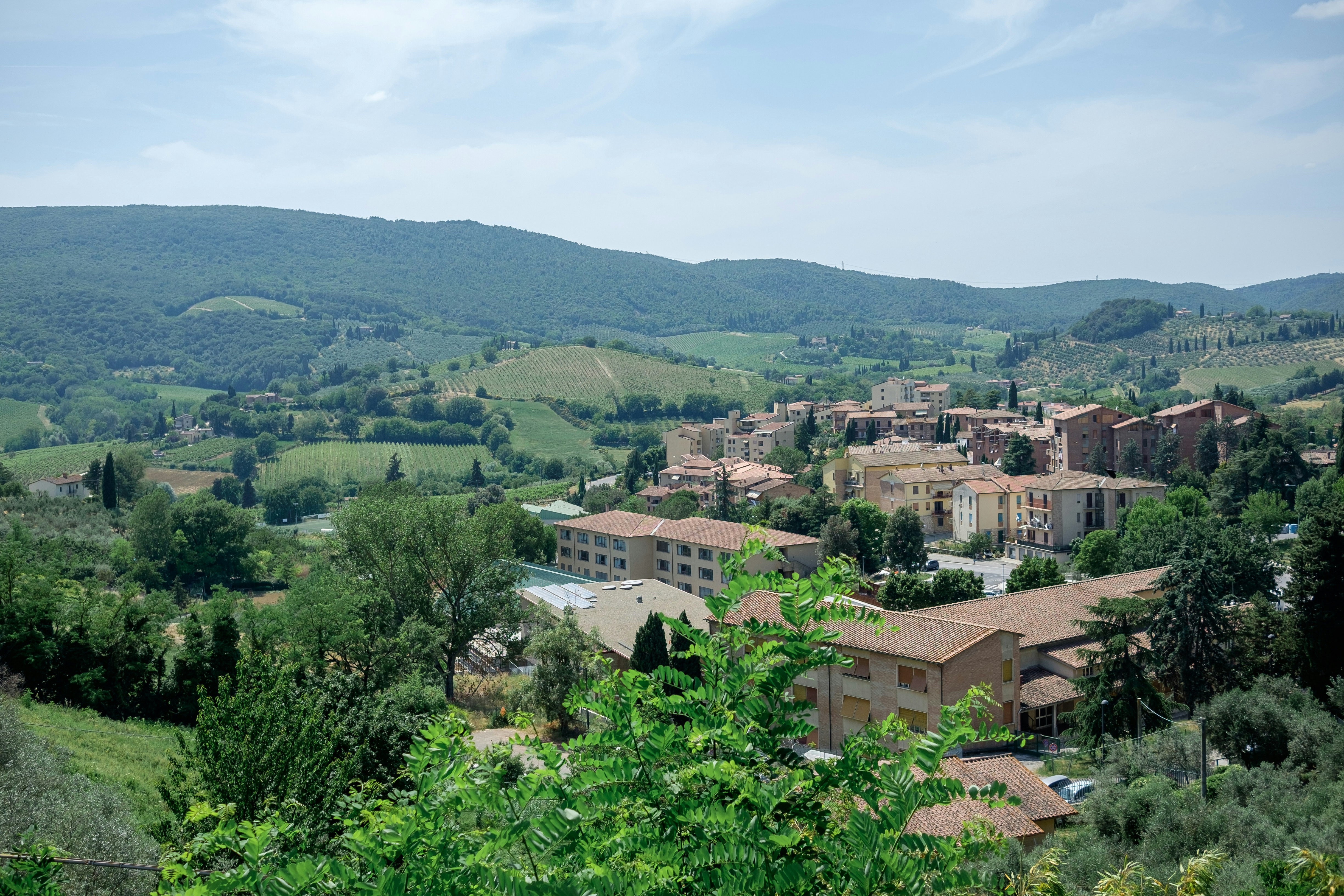 Rolling green hills and a quaint village stretch under a vast sky in the Tuscan countryside.